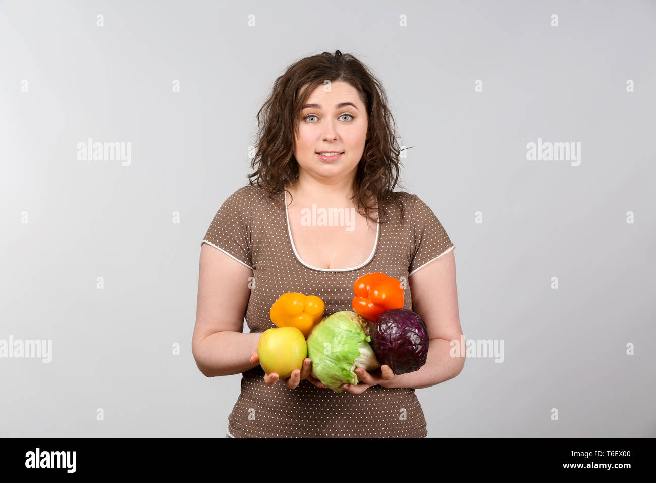 Young stout woman with fresh vegetables and fruit on grey background ...