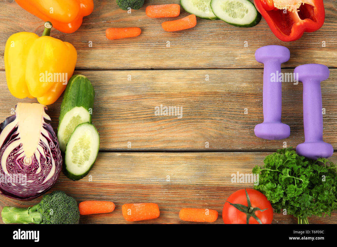 Frame made of fresh vegetables and dumbbells on wooden background. Diet ...