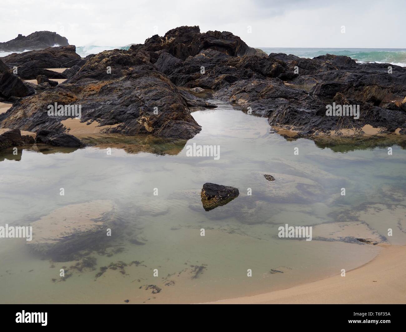 Rock pool at the Beach, blue green water, as waves crash into the rocks ...