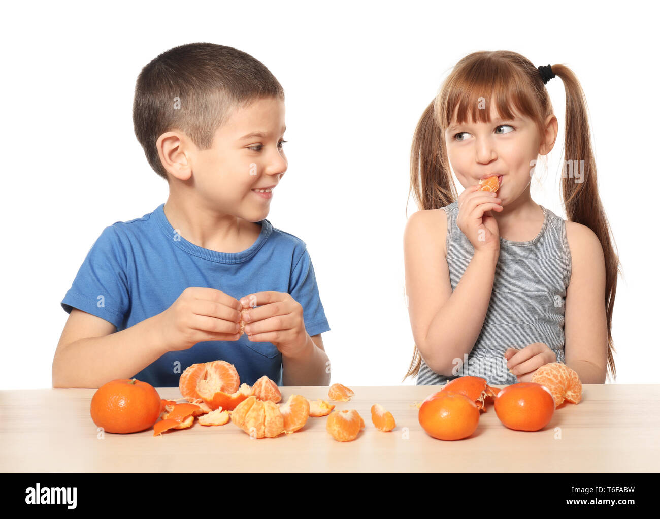 Cute little children eating citrus fruit at table on white background ...