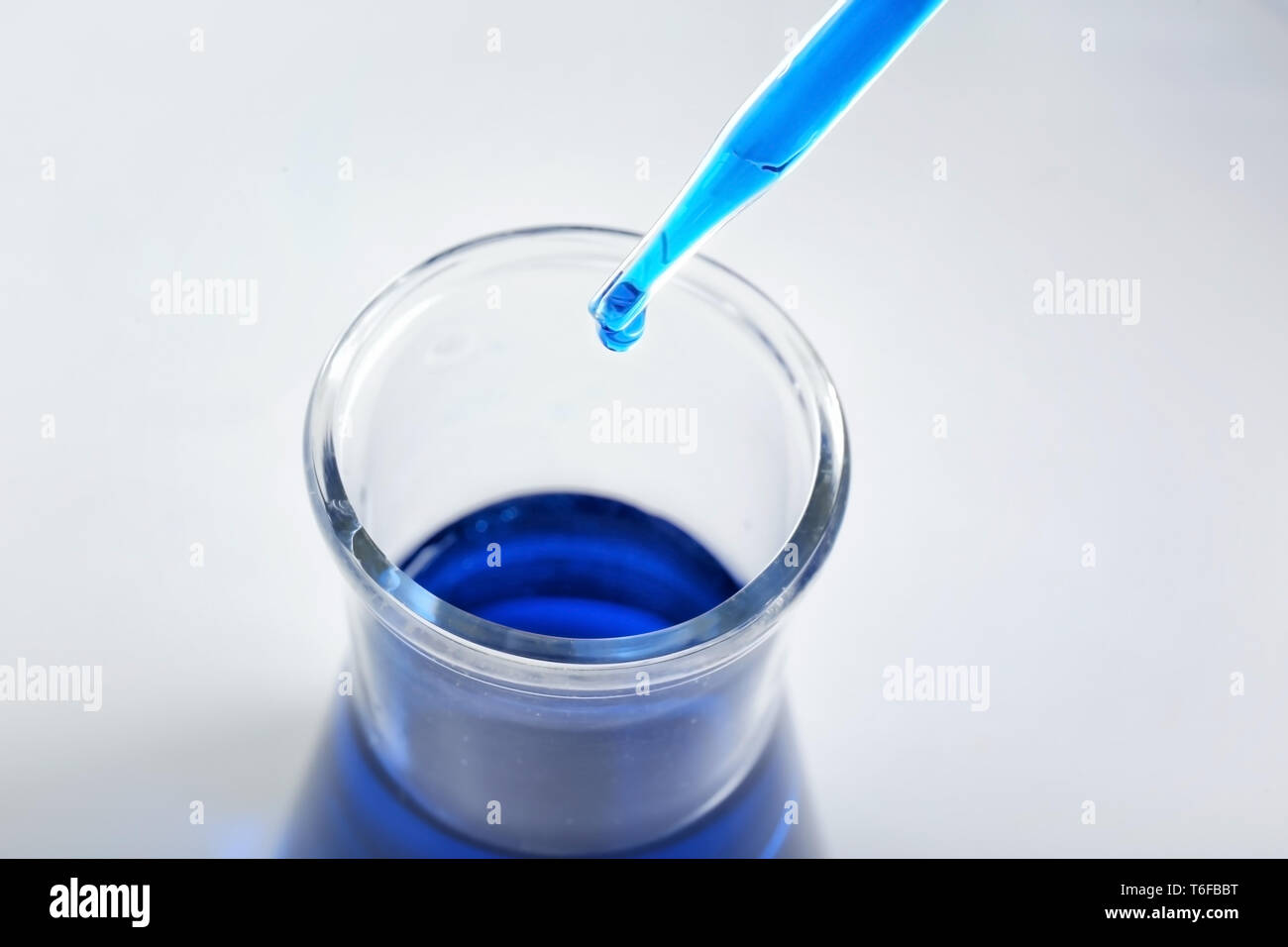 Dripping blue liquid into flask on light background Stock Photo - Alamy