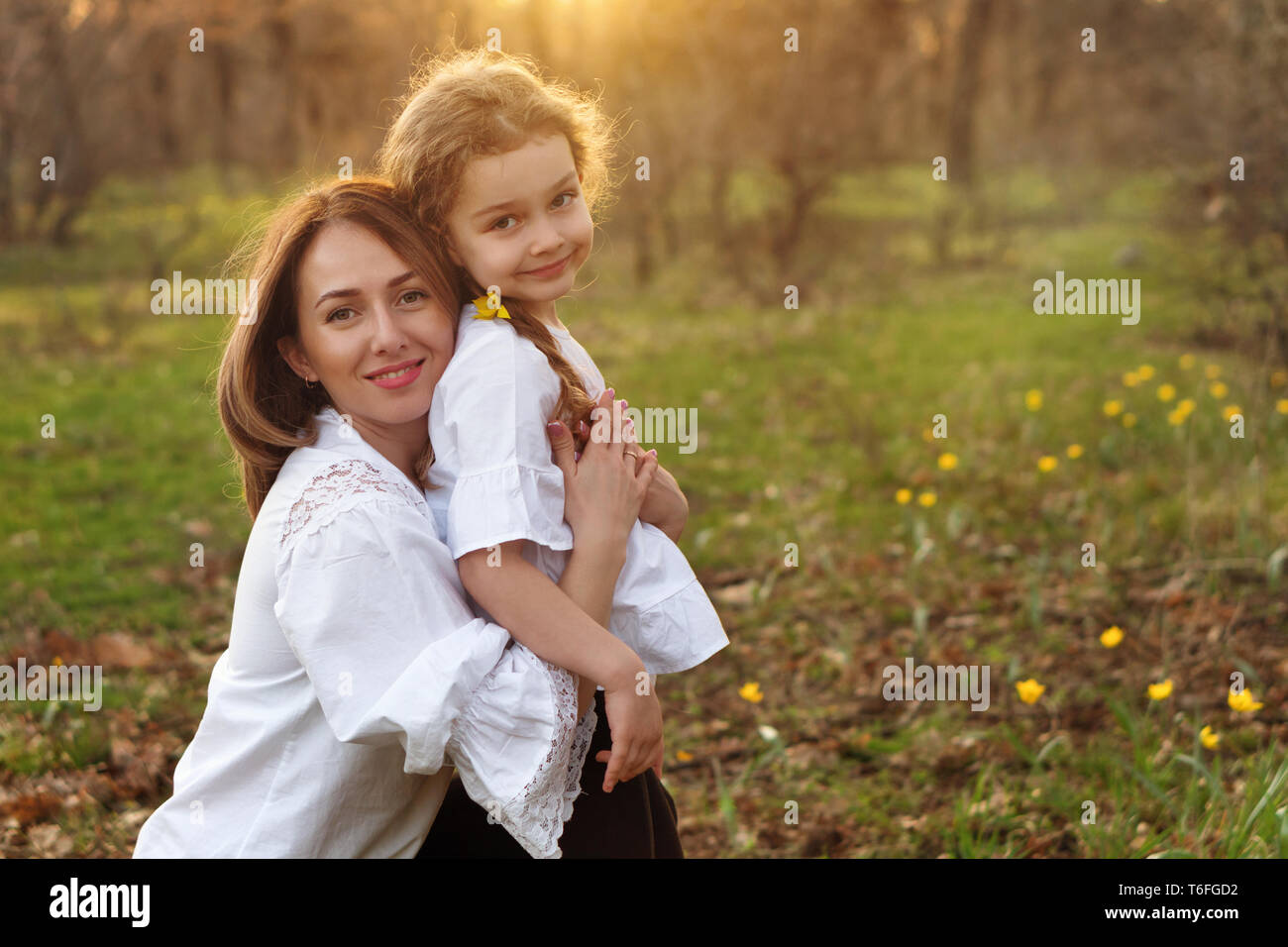 Family cuddle outdoors at sunset. Young charming mother is embracing a ...