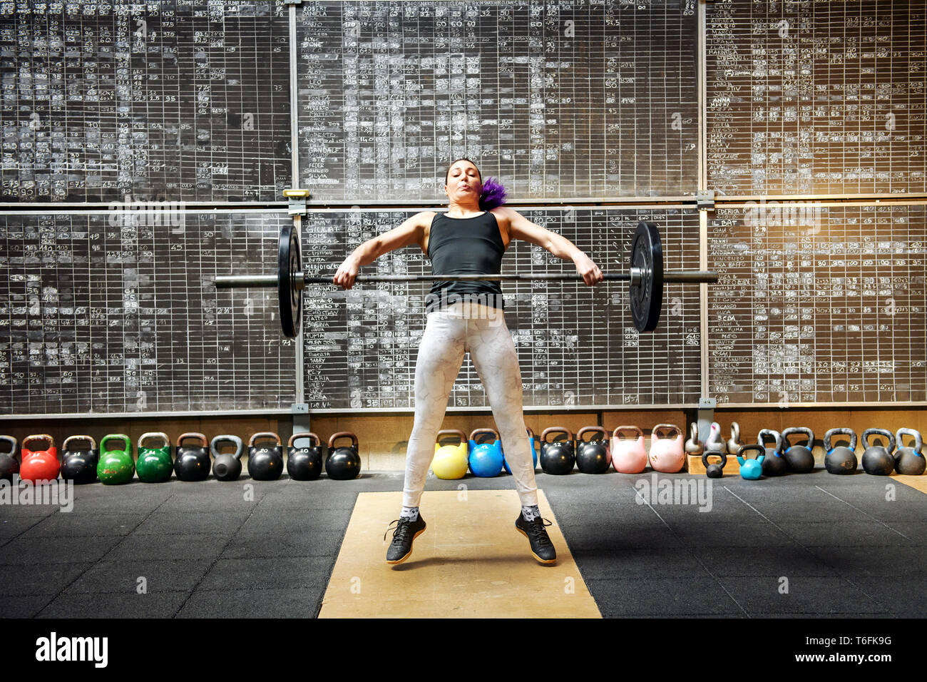 Young woman athlete doing the snatch with a barbell snatching it off ...