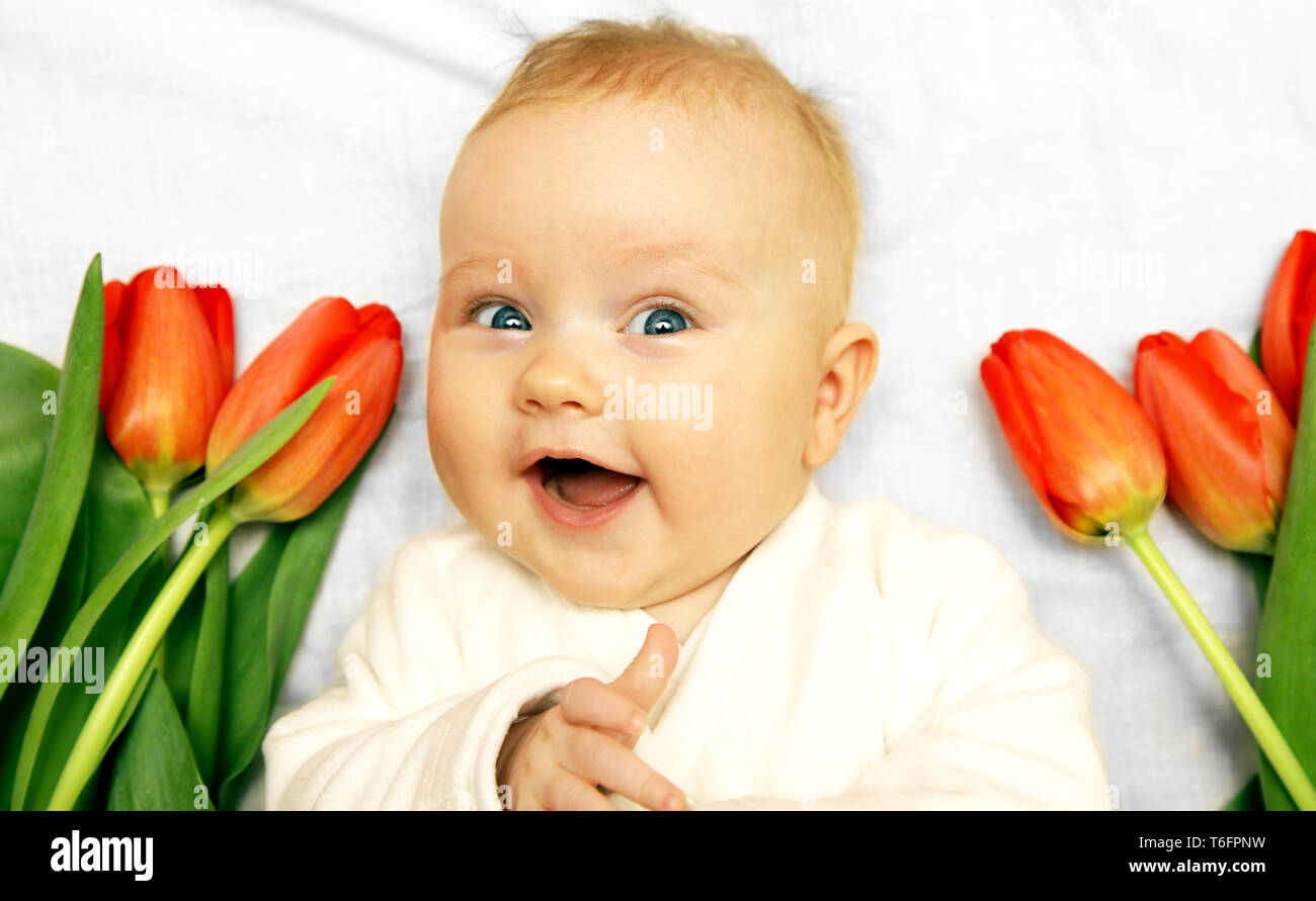 newborn baby girl boy laughing and showing thumb up among red tulips ...