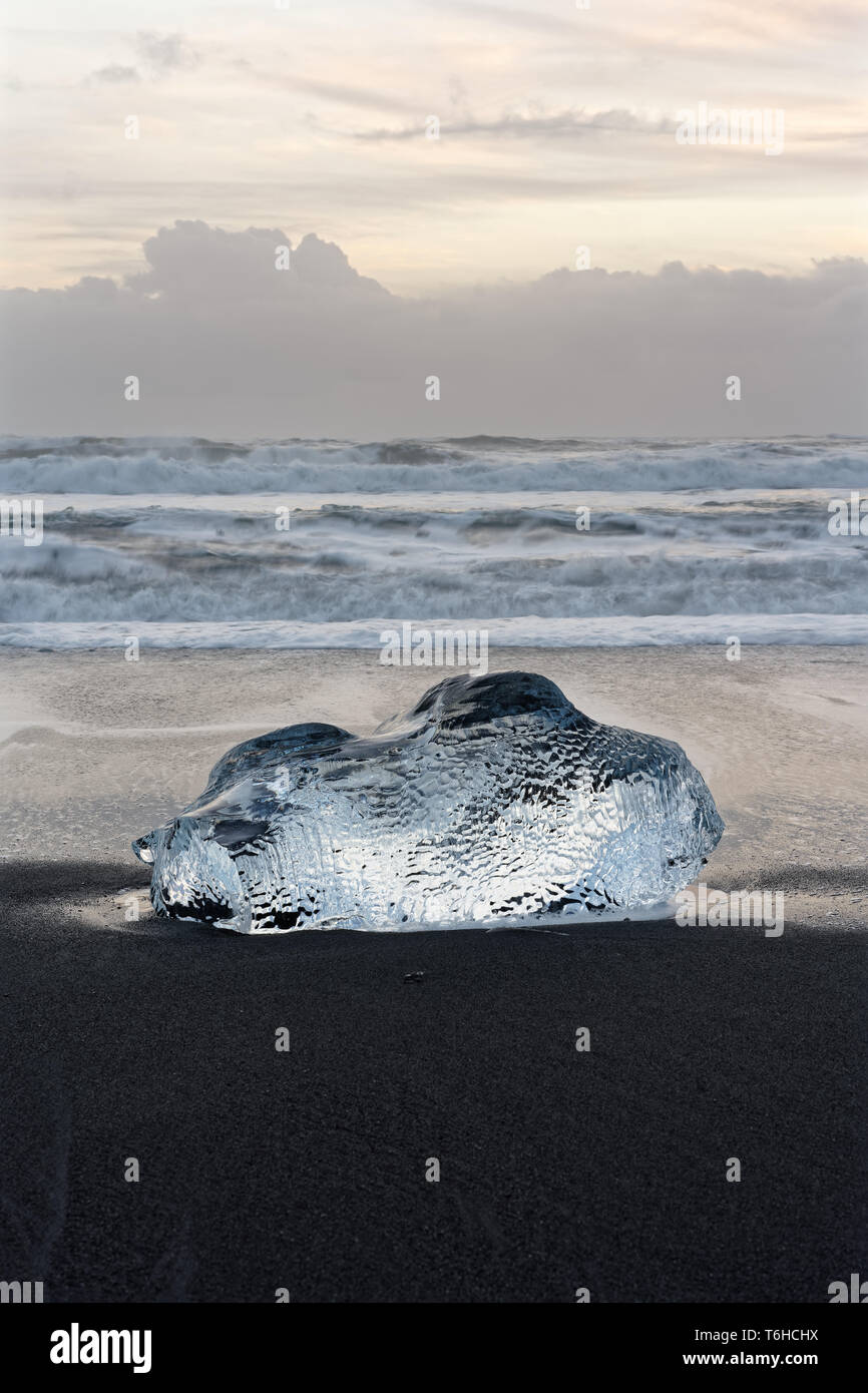 Round ice block in blue shades on a beach with strong surf, above it a ...