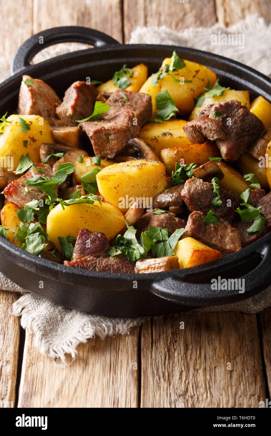 Rustic style fried pork with potatoes and mushrooms close-up in a pan ...