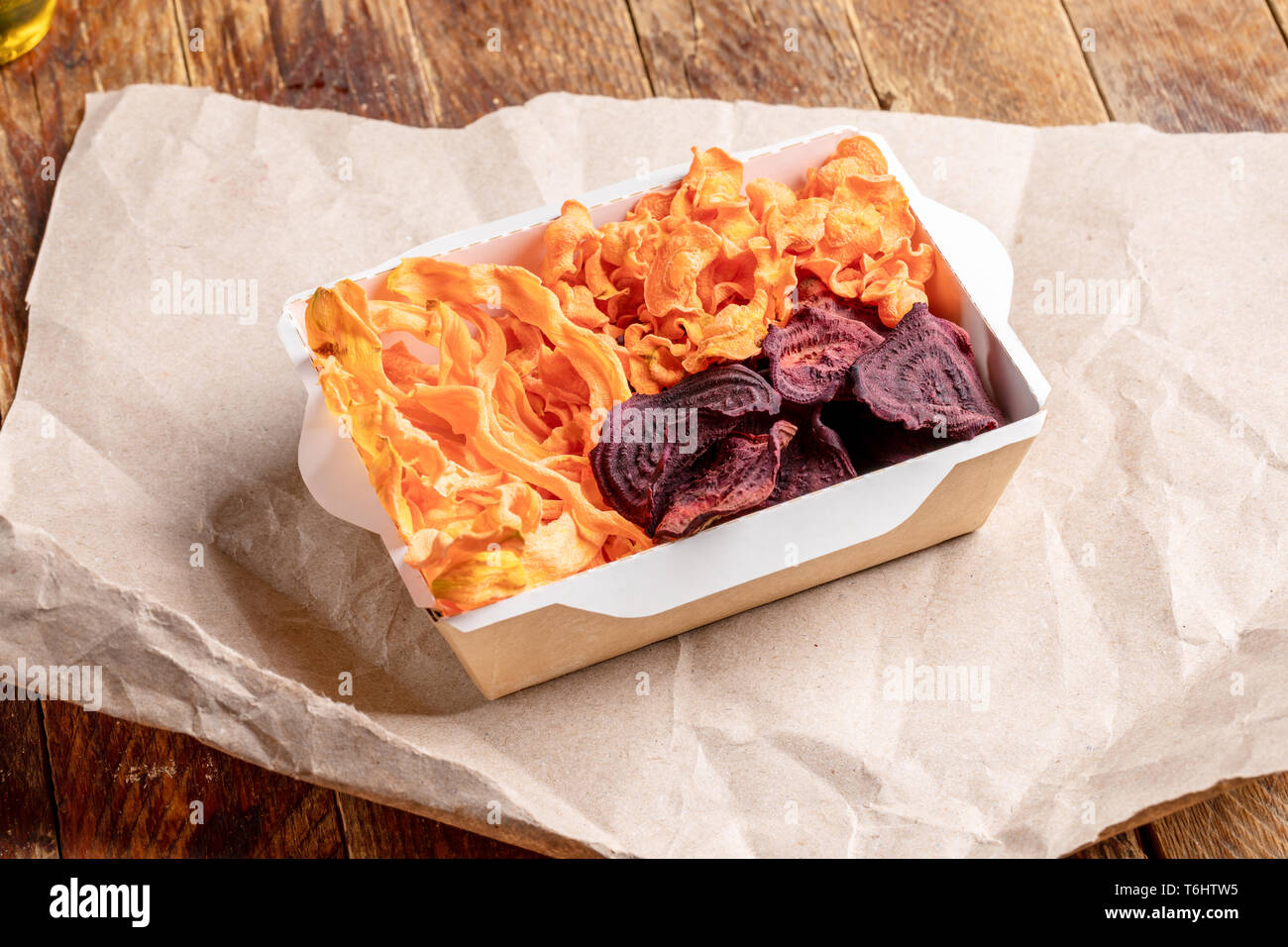 Paper box with vegetable chips on wrapping paper on old wooden table ...
