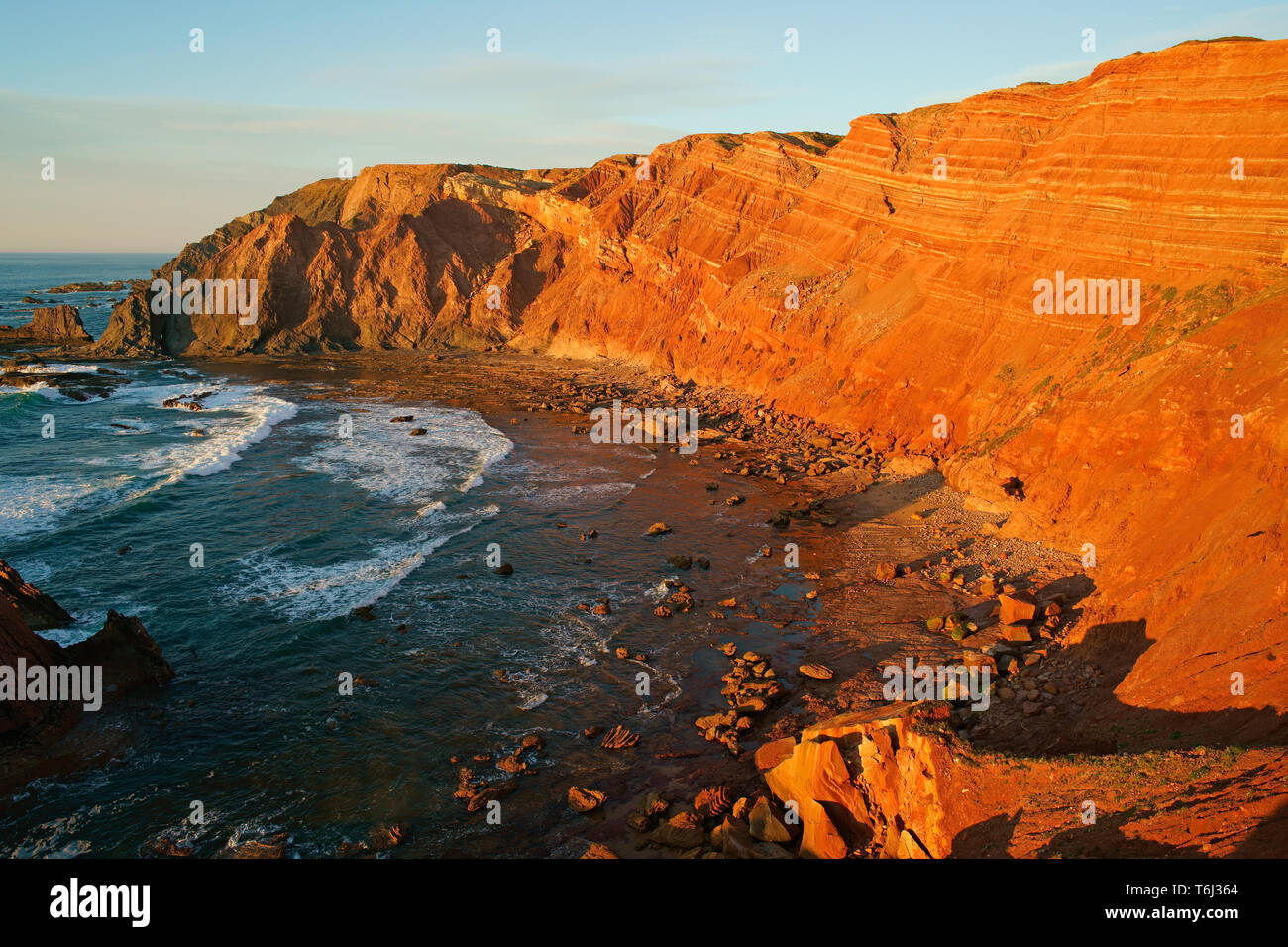 Glowing red sea cliff just before sunset. Near telheiro Beach, Vila do ...