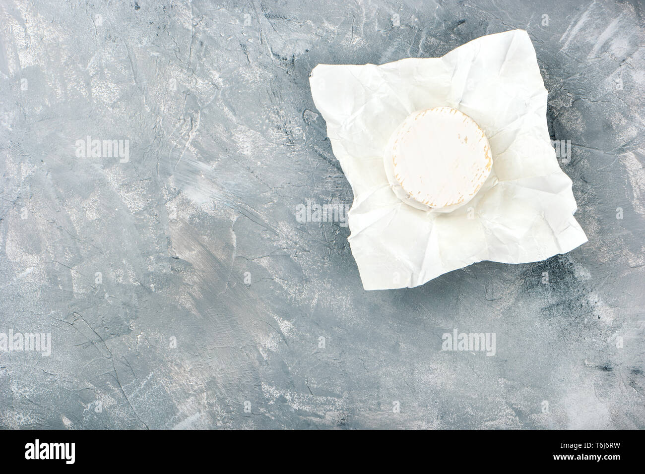 Round brie cheese in open paper package on grey concrete background ...