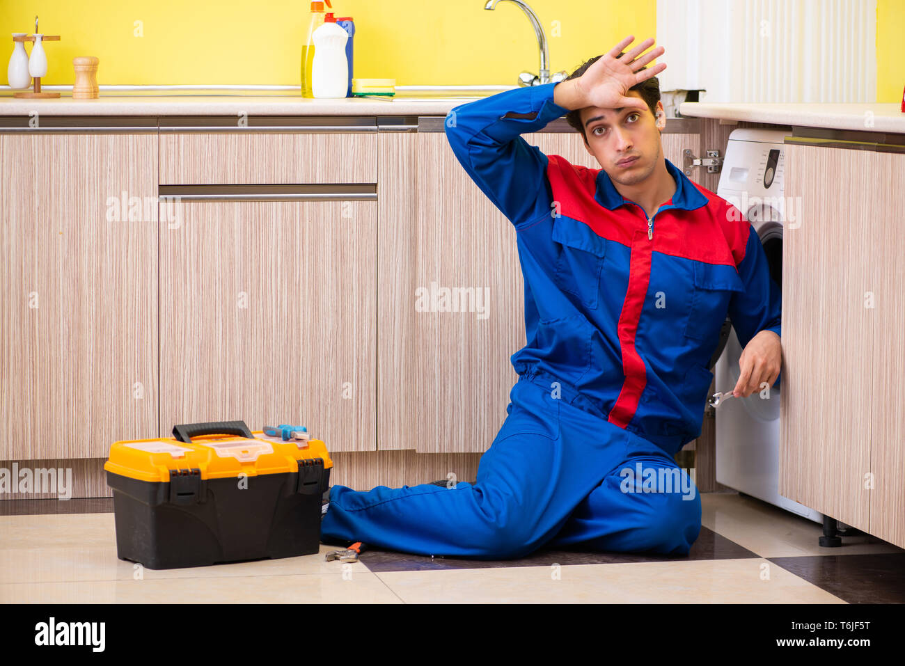 Repairman repairing washing machine in the kitchen Stock Photo - Alamy