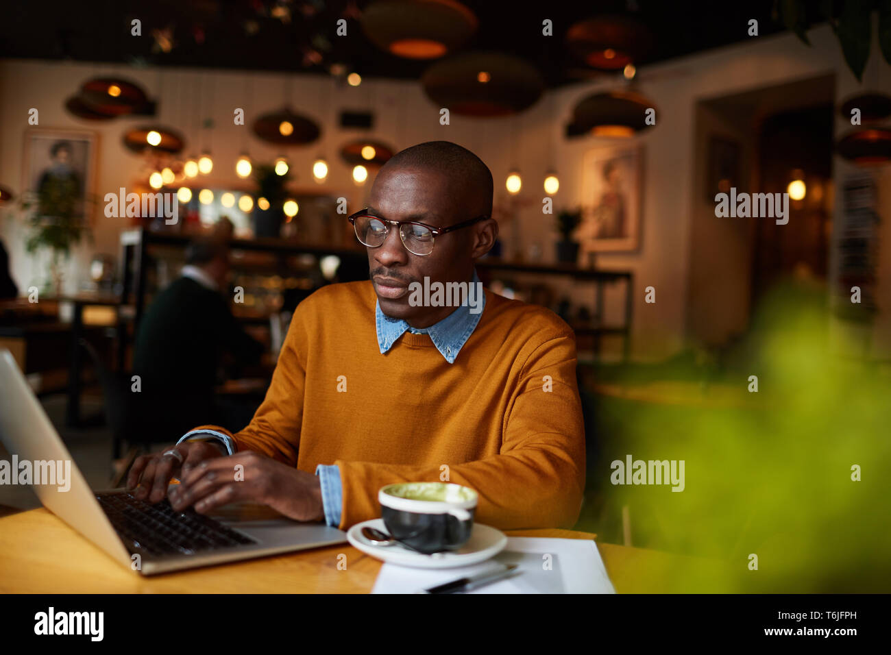 Warm toned portrait of contemporary African-American man using laptop ...