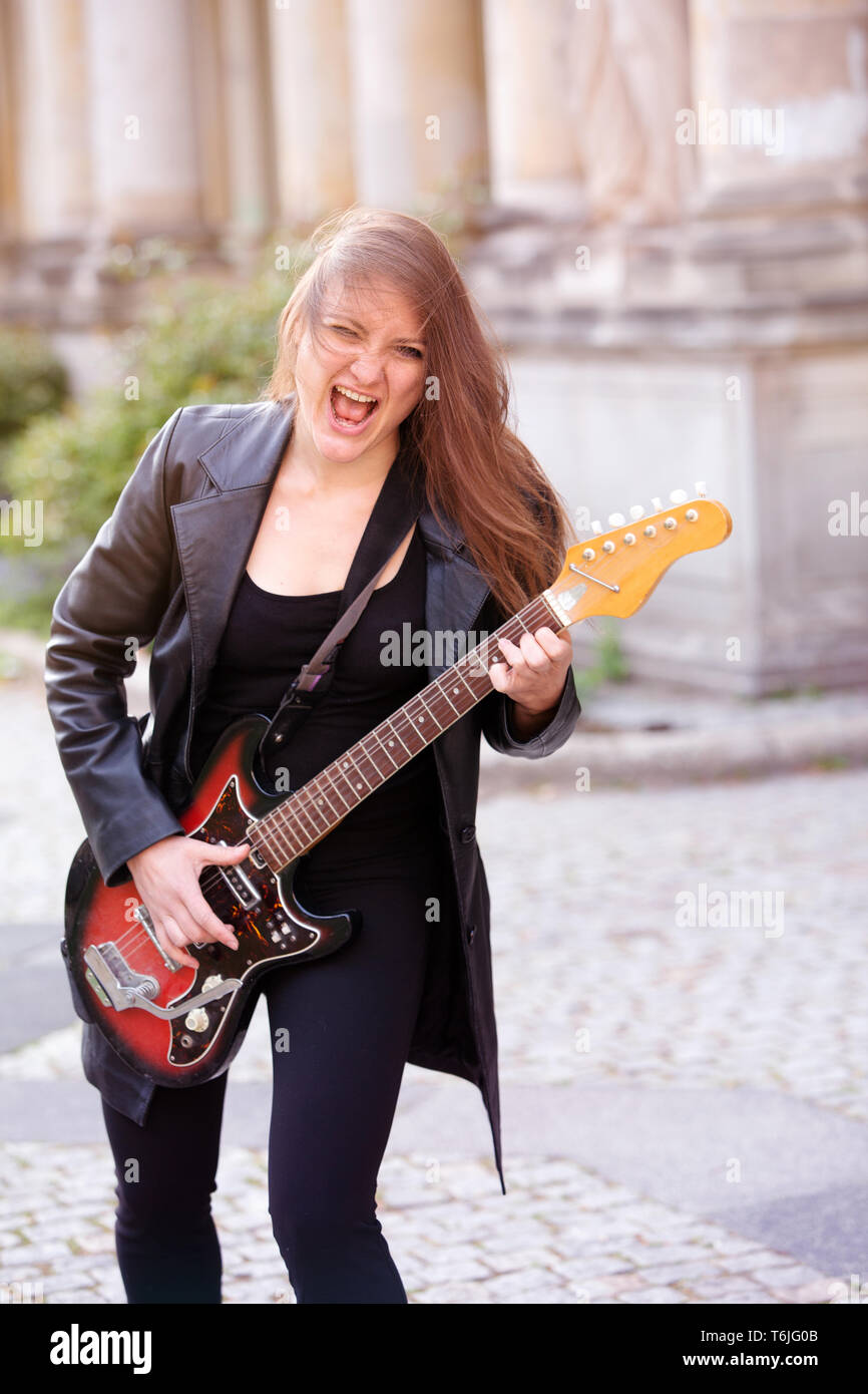 young brunette woman in black leather jacket playing the guitar ...
