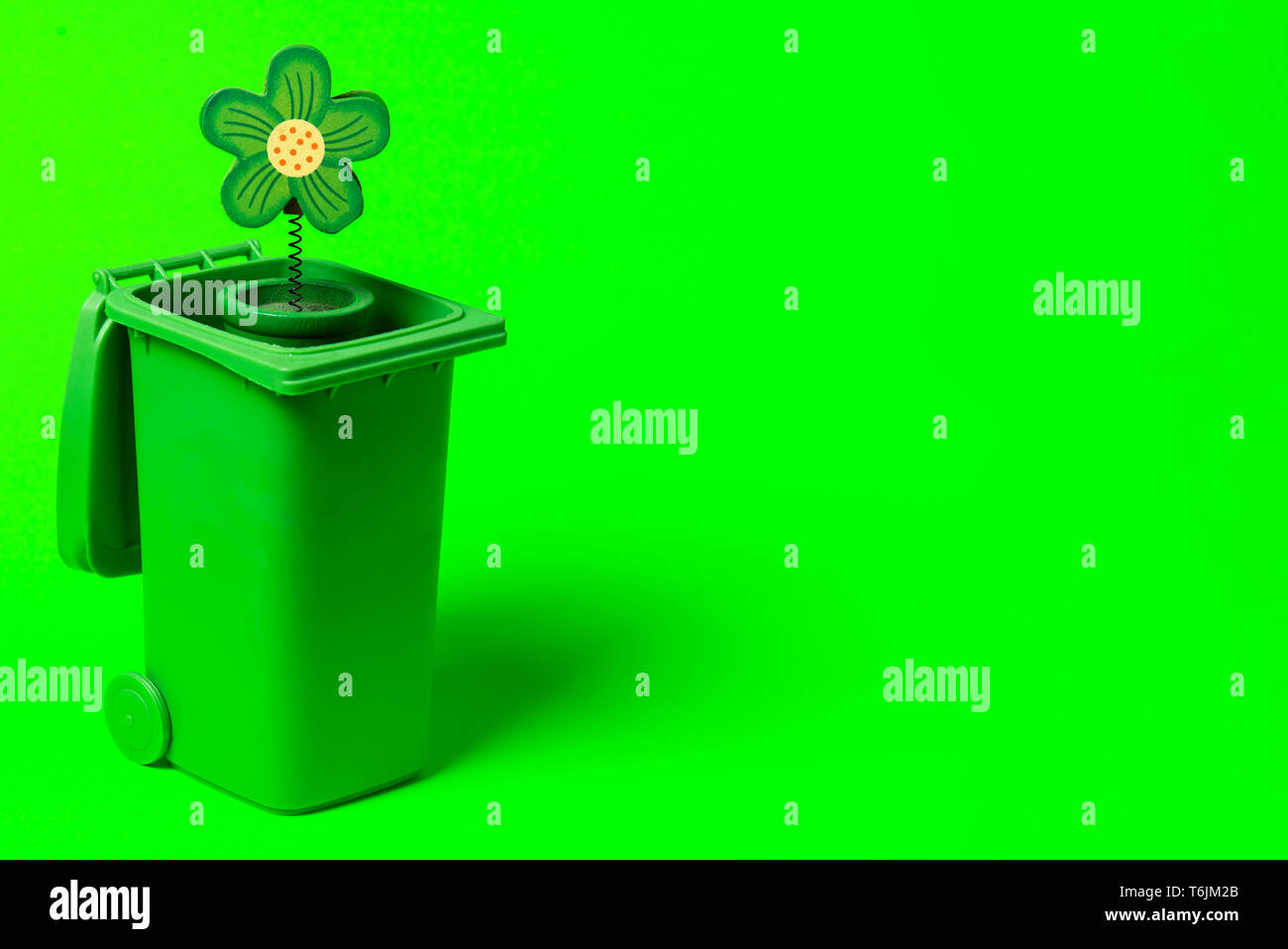 Green trash can with flowers on a green background Stock Photo - Alamy