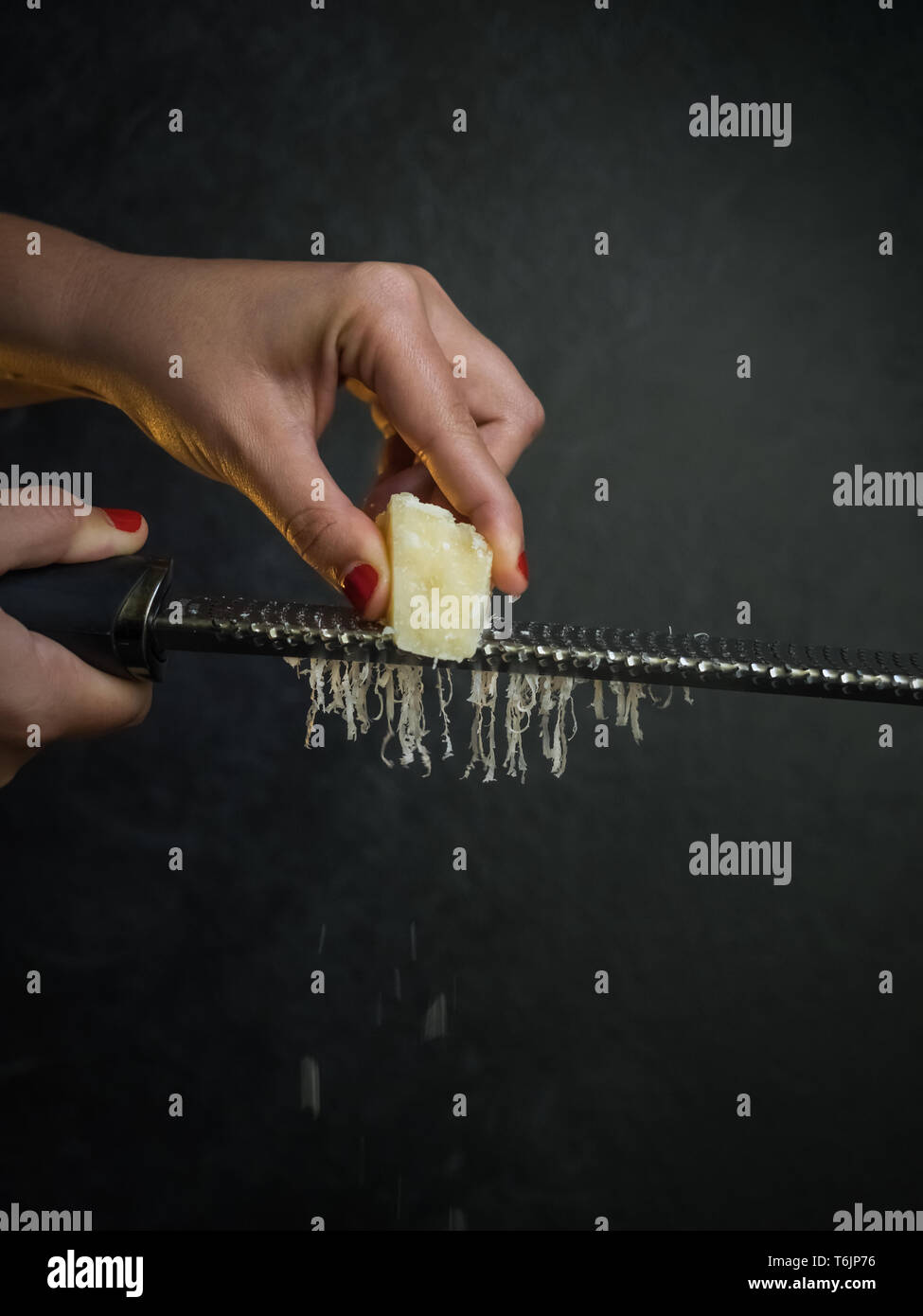 Hand of a woman grating parmesan cheese on a black background. Dark ...