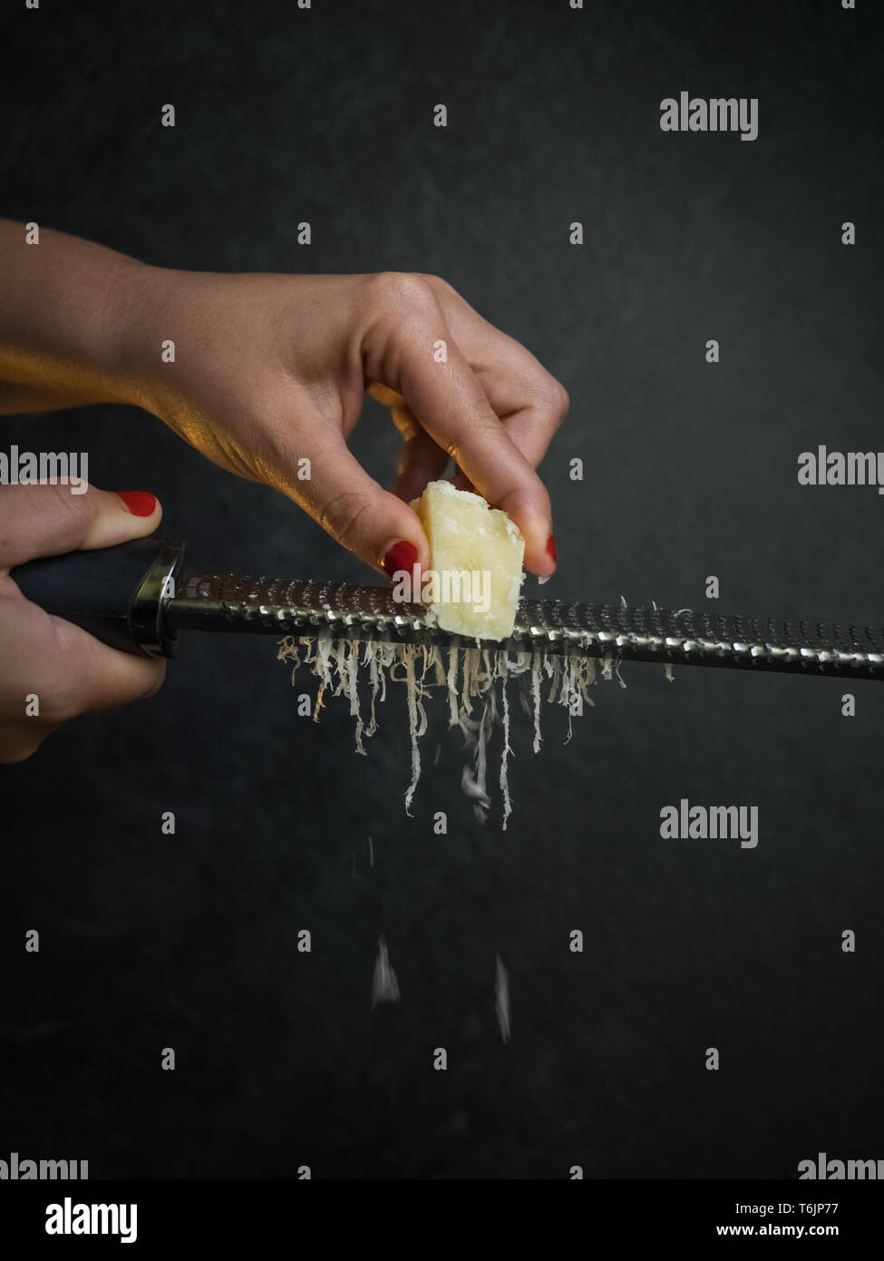 Hand of a woman grating parmesan cheese on a black background. Dark ...