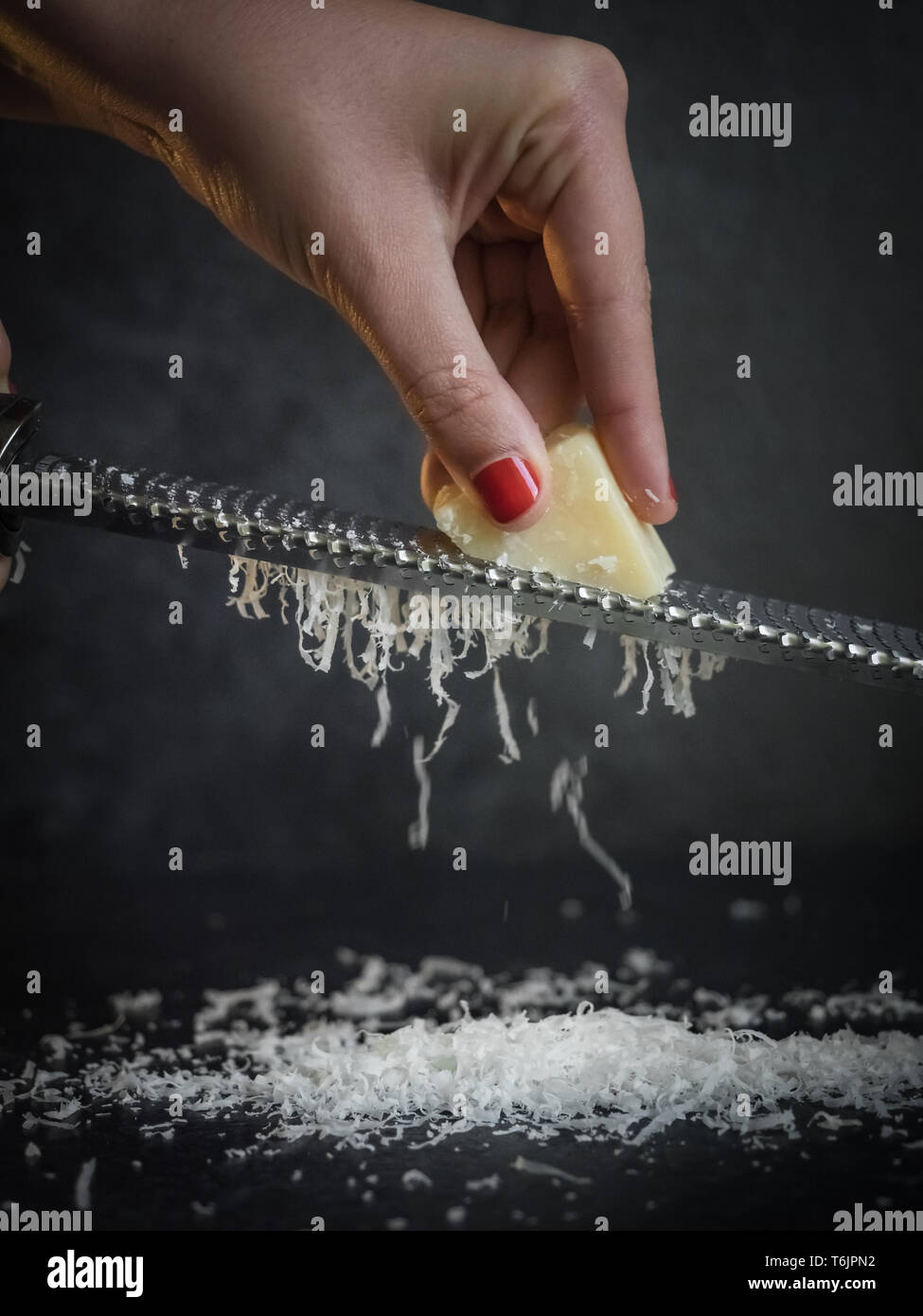 Hand of a woman grating parmesan cheese on a black background. Dark ...