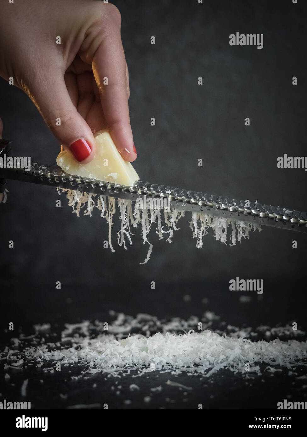 Hand of a woman grating parmesan cheese on a black background. Dark ...