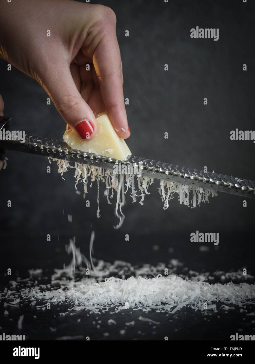 Hand of a woman grating parmesan cheese on a black background. Dark ...