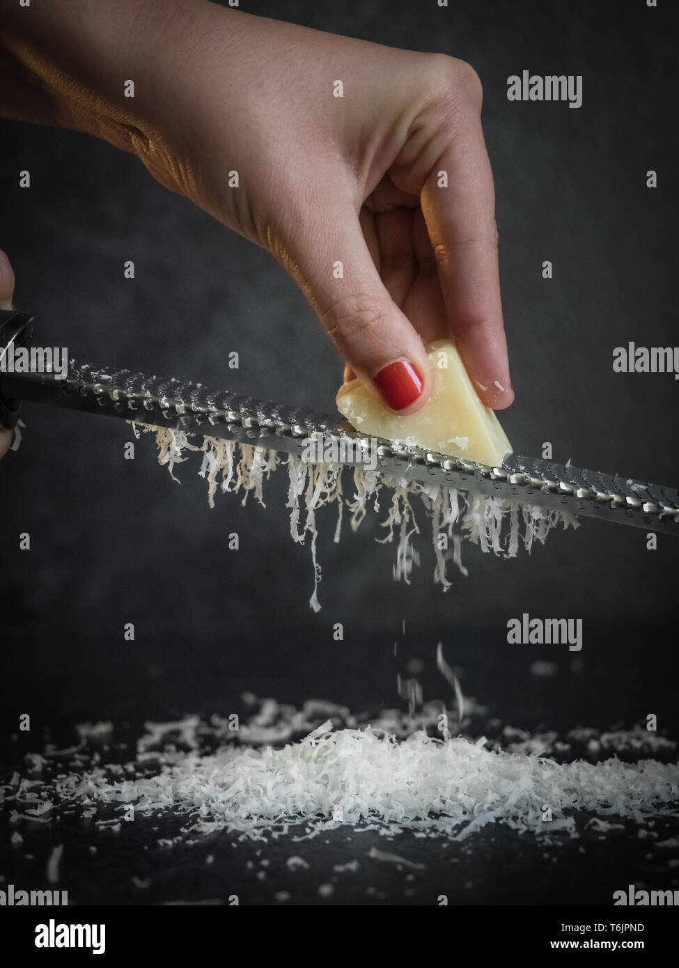Hand of a woman grating parmesan cheese on a black background. Dark ...
