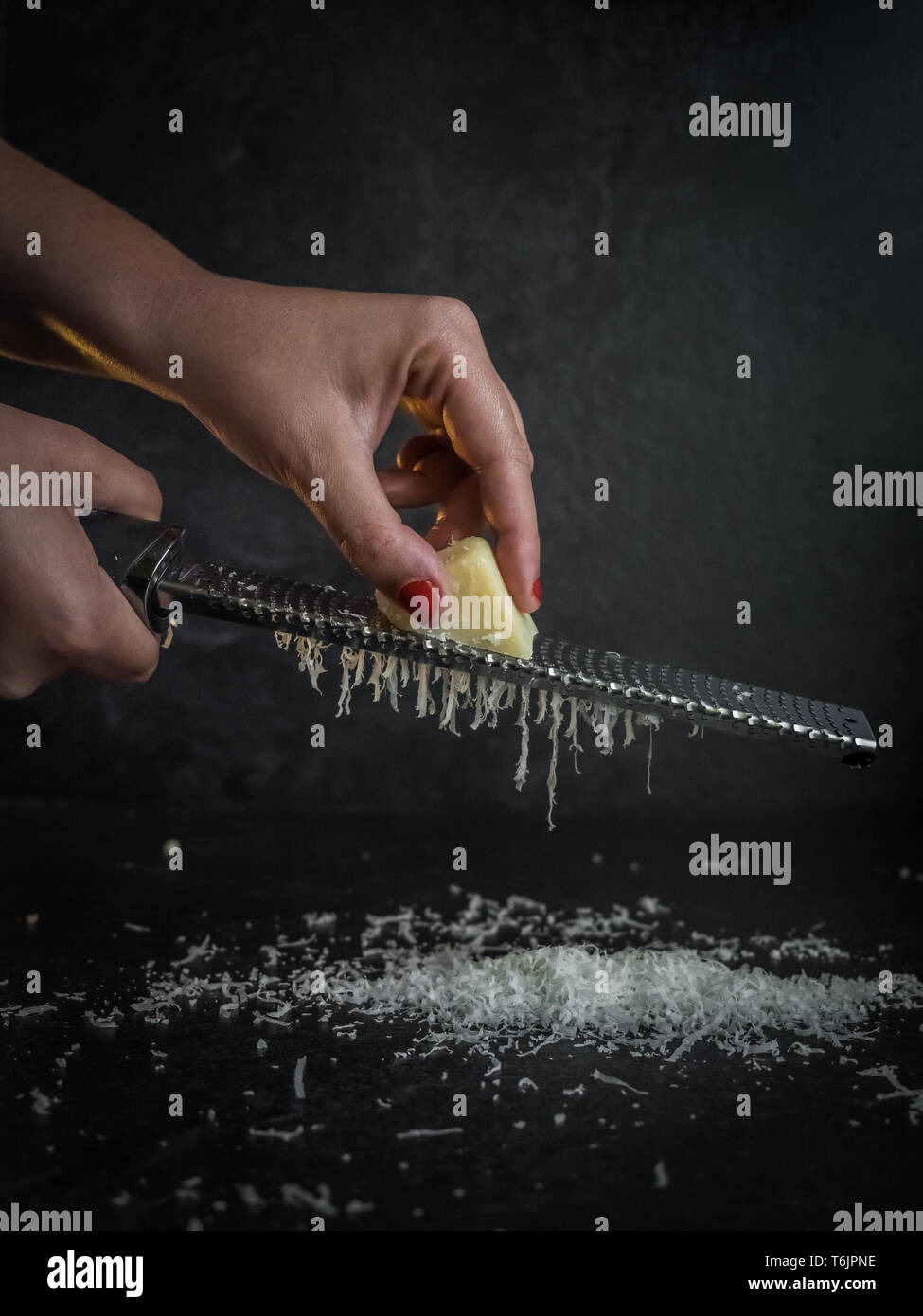 Hand of a woman grating parmesan cheese on a black background. Dark ...
