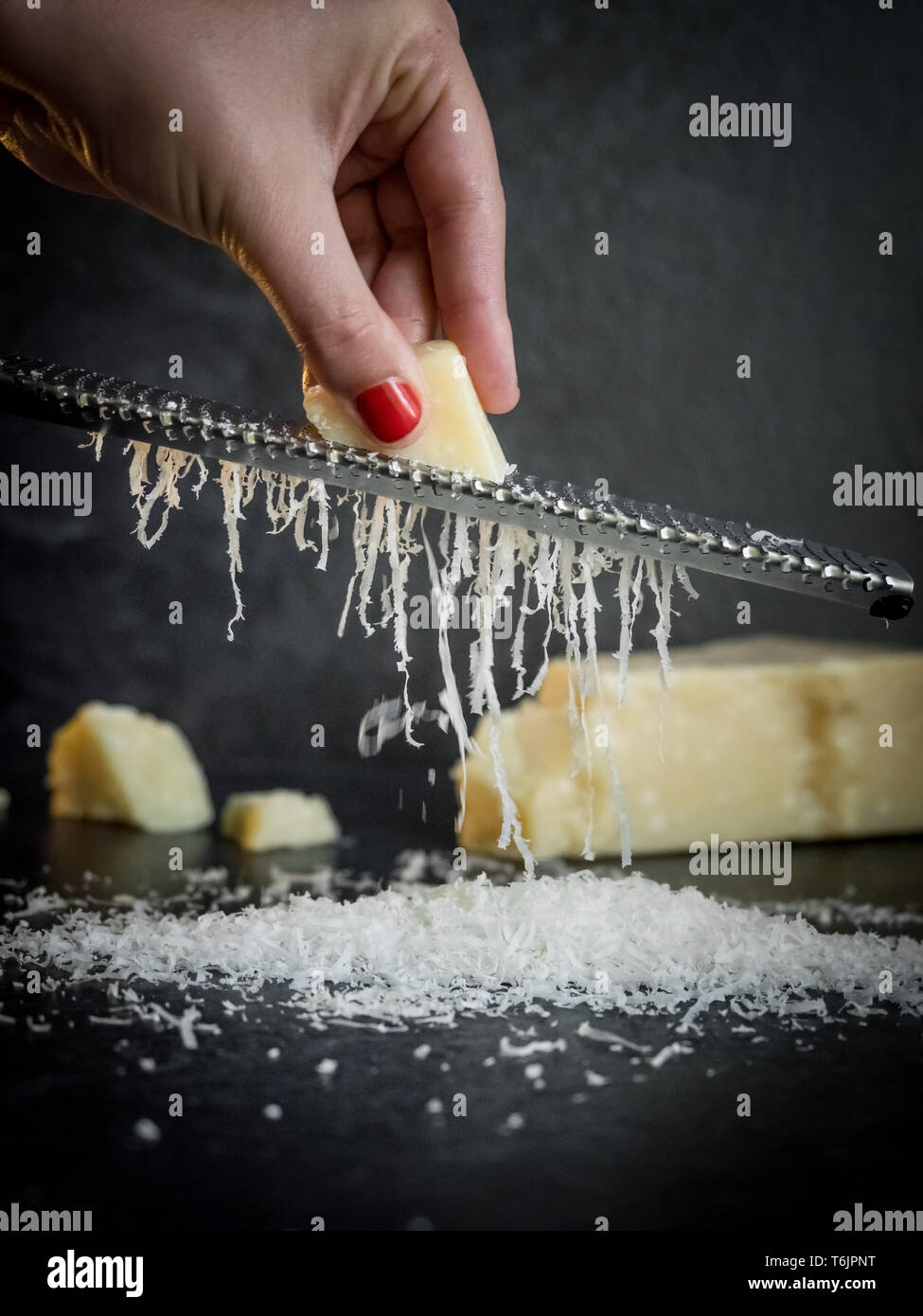 Hand of a woman grating parmesan cheese on a black background. Dark ...