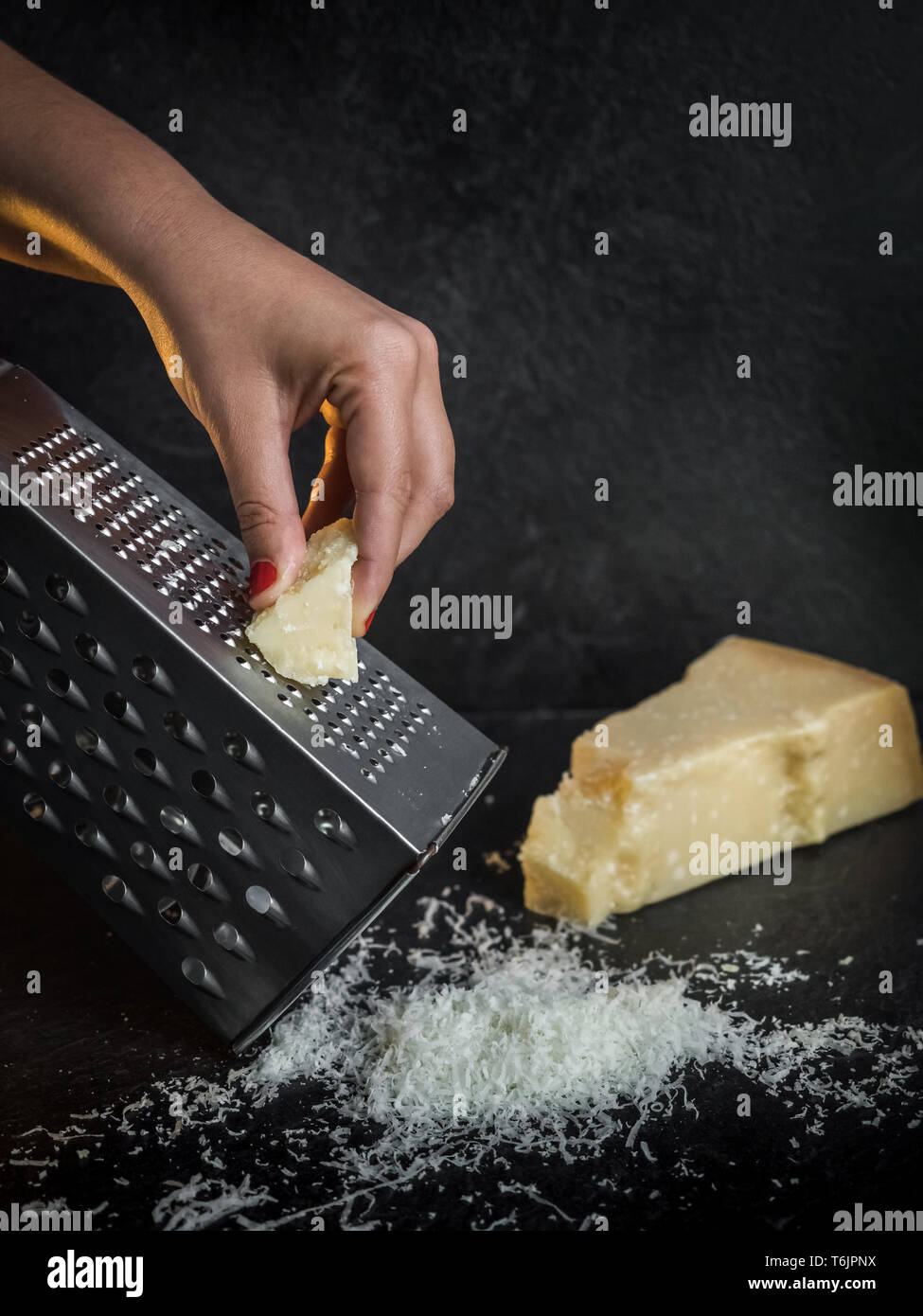 Hand of a woman grating parmesan cheese on a black background. Dark ...