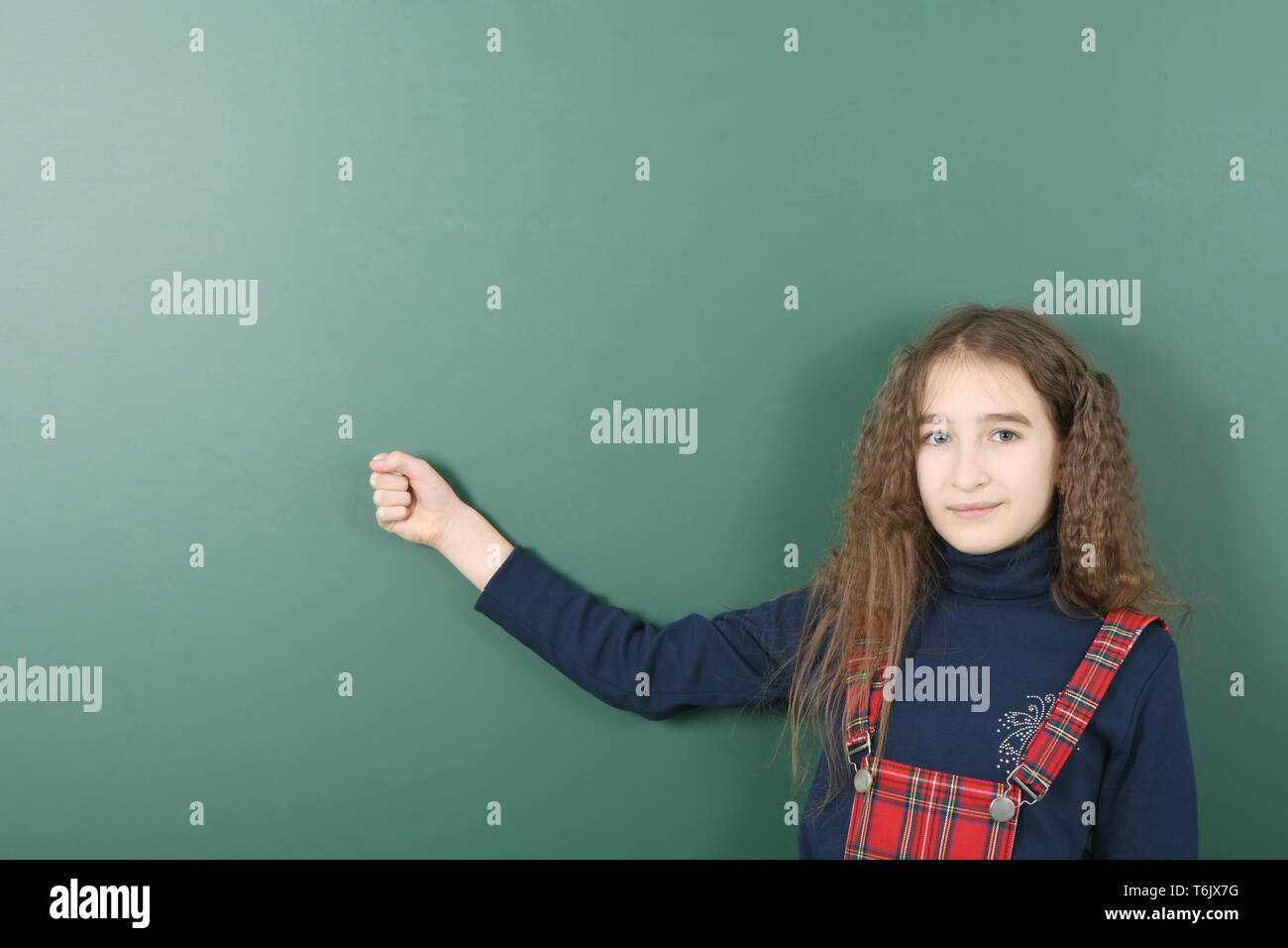 Schoolgirl near green school board. Young playful girl shows finger ...