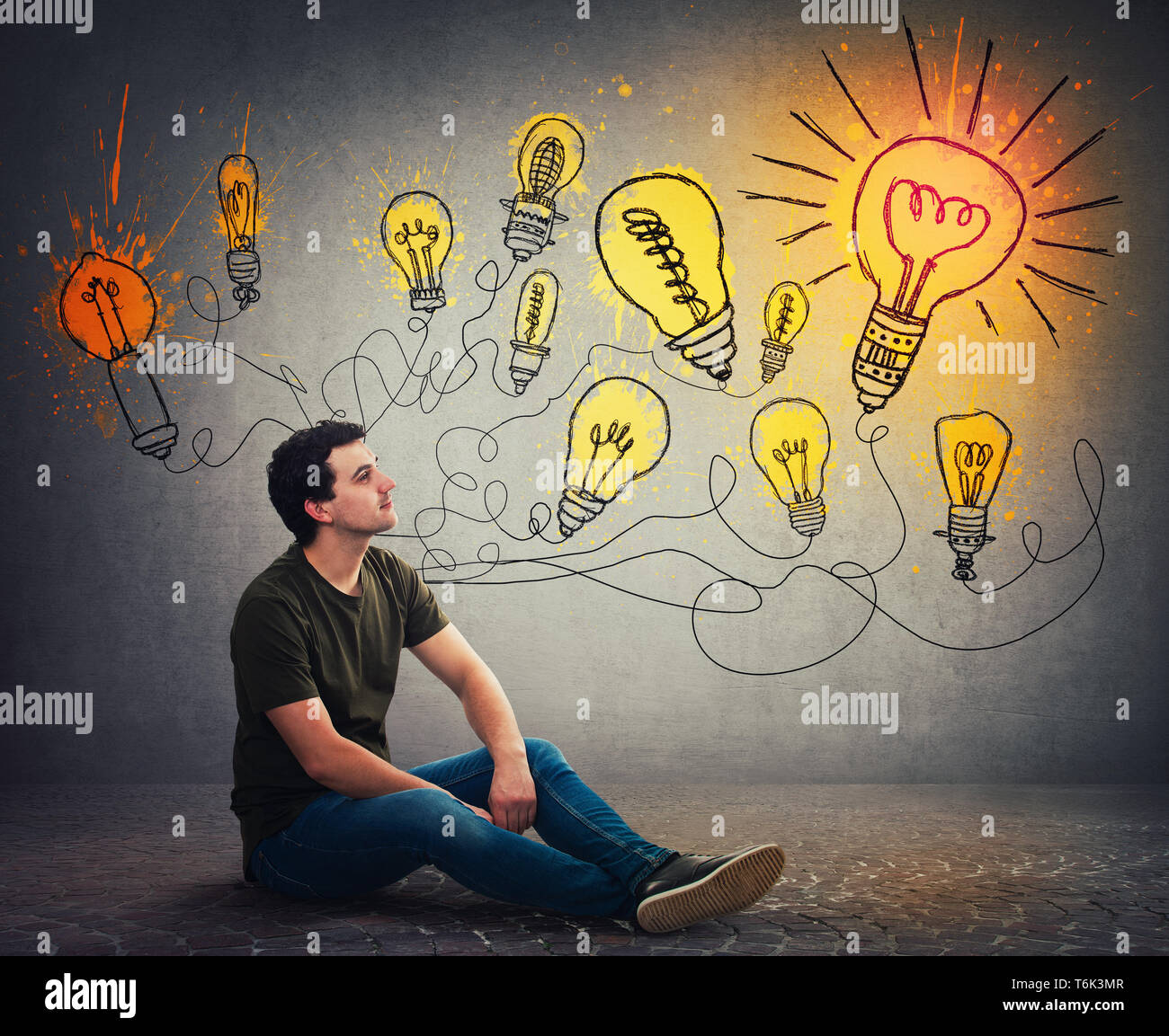 Relaxed man sitting on the floor smiling looking at bright lightbulbs ...