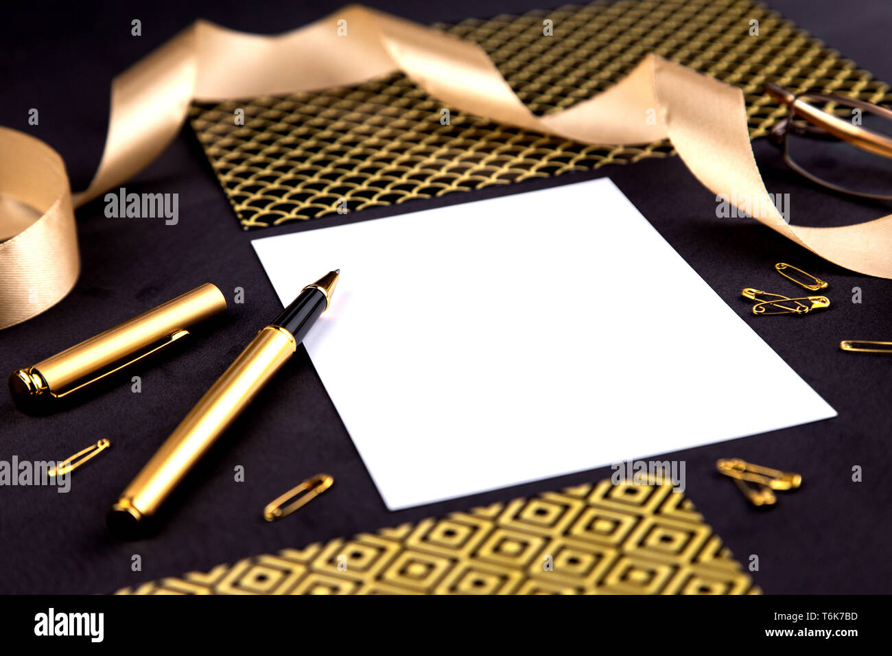 Gold pen, ribbon, paper clips and stationery on a black background with ...