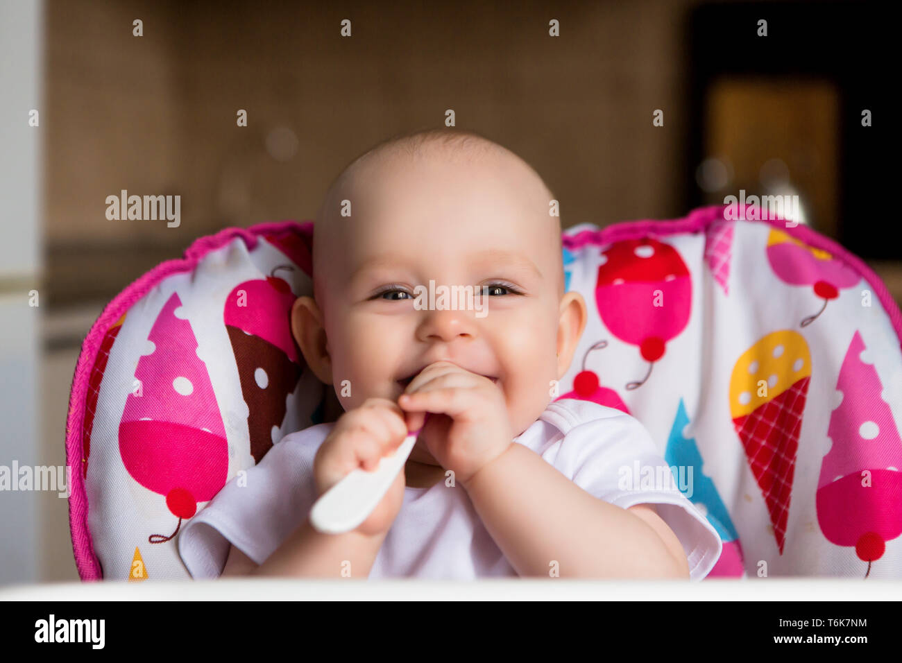 Baby in the kitchen in a baby chair holding a spoon and smiling.Sweet ...
