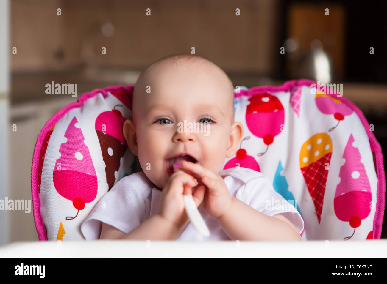 Baby in the kitchen in a baby chair holding a spoon and smiling.Sweet ...