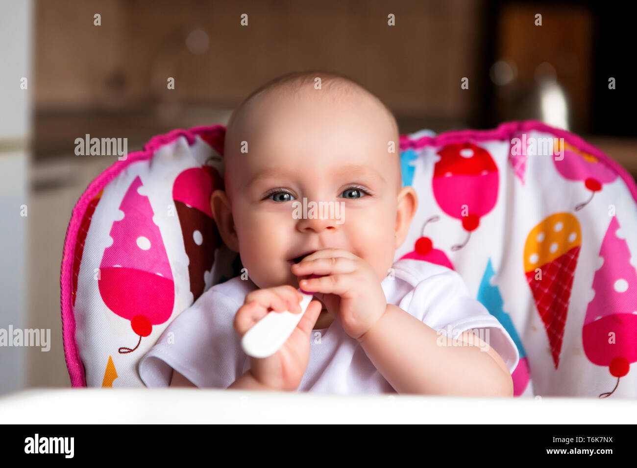 Baby in the kitchen in a baby chair holding a spoon and smiling.Sweet ...