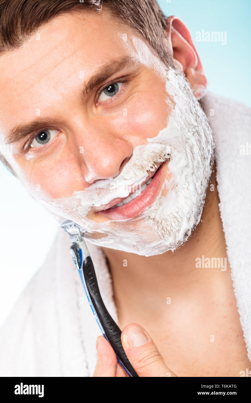 Young man shaving using razor with cream foam. Handsome guy removing face beard hair. Skin care ...