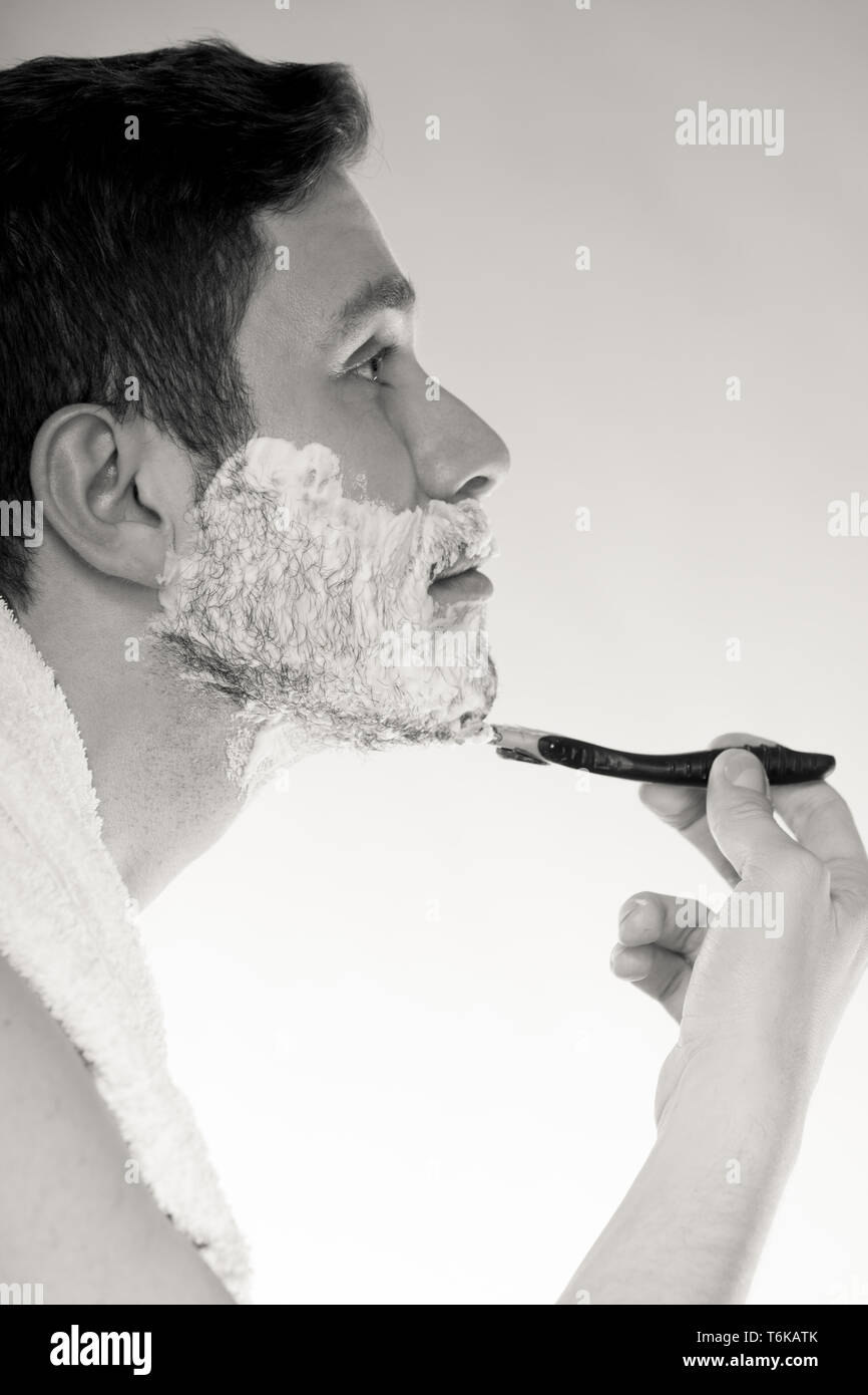 Young man shaving using razor with cream foam. Handsome guy removing face beard hair. Skin care ...