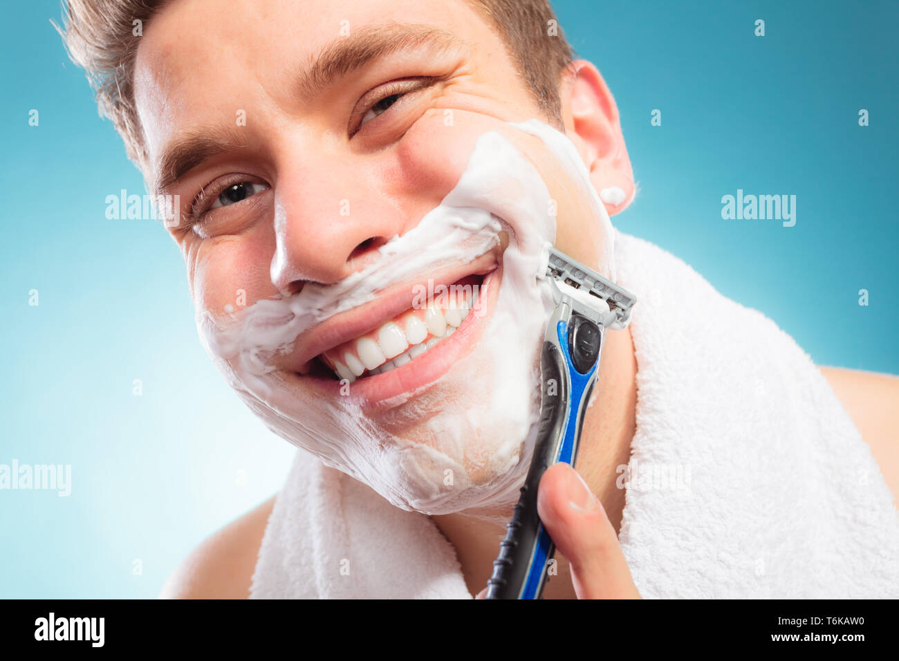 Happy smiling man shaving using razor with cream foam. Handsome guy removing face beard hair ...