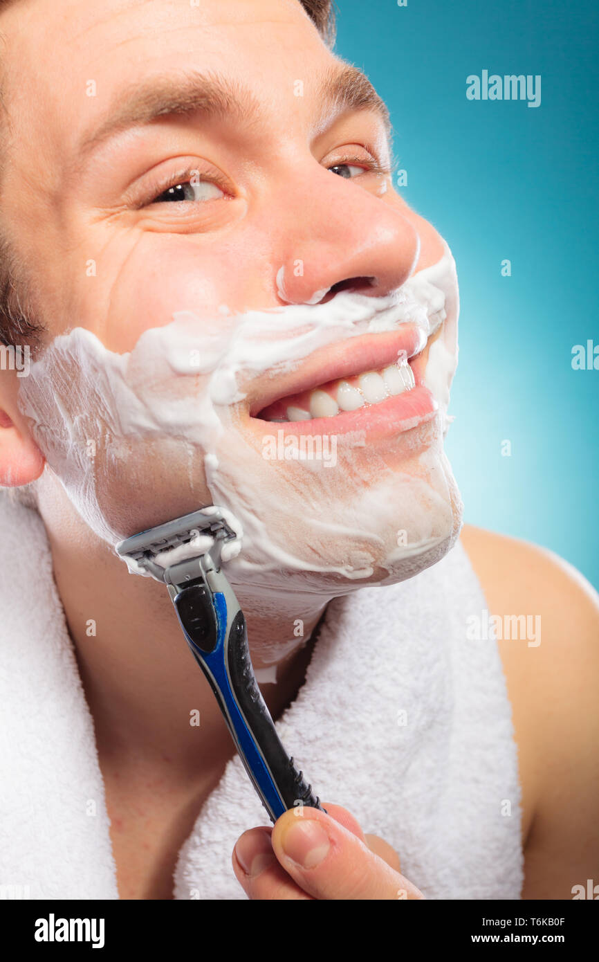 Happy smiling man shaving using razor with cream foam. Handsome guy ...