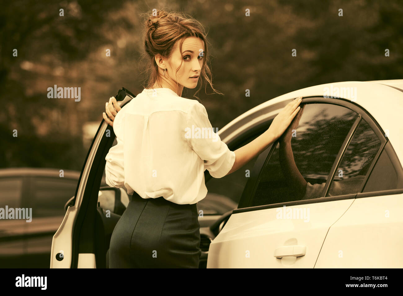 Young fashion business woman next to her car Stylish female model with bun up do hair wearing ...