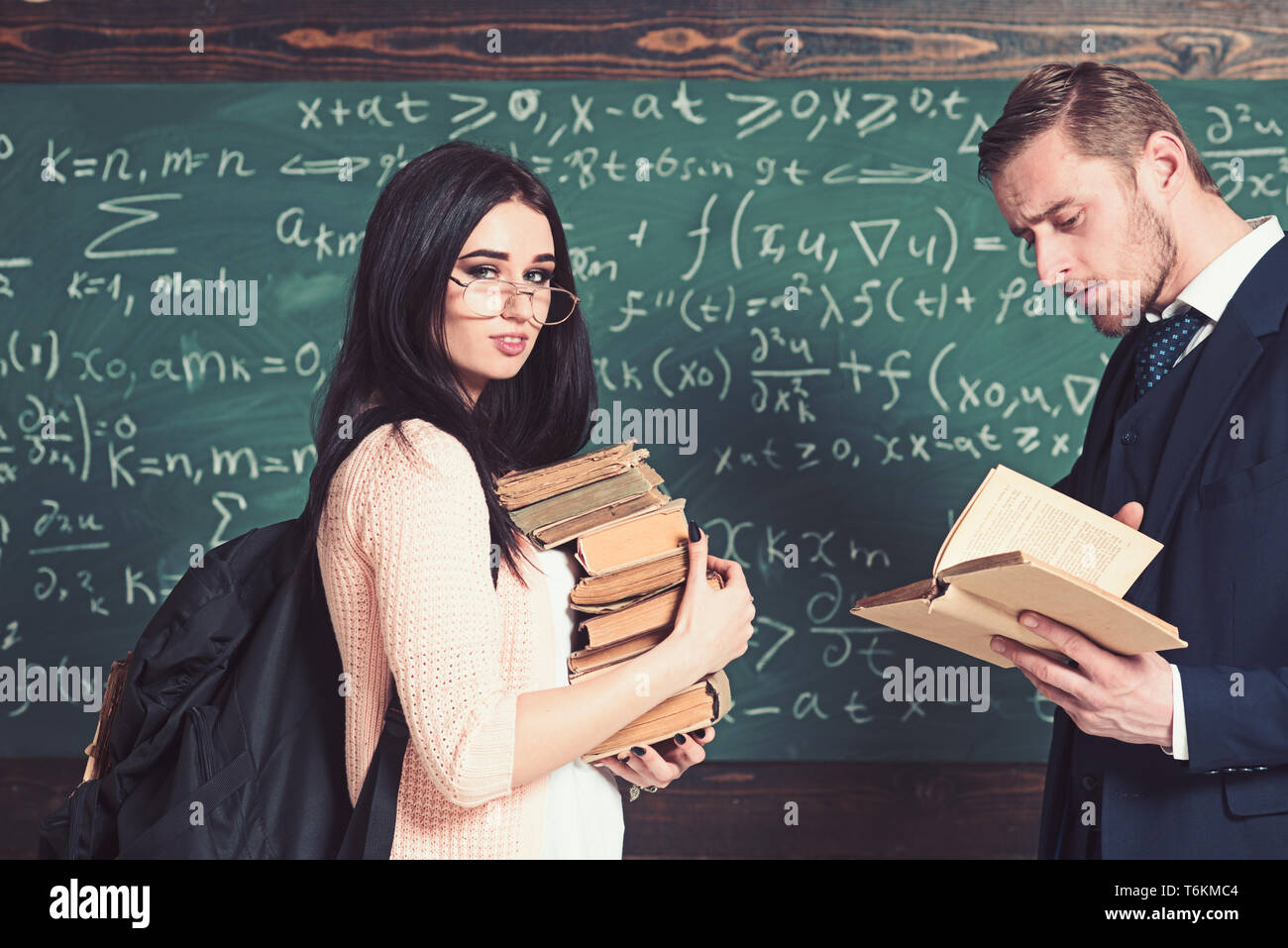 Smiling girl with heap of books standing in front of her stylish young ...