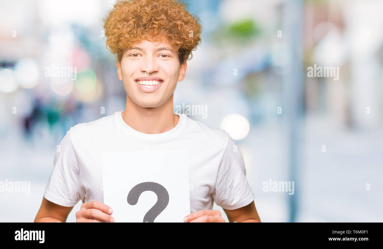 Young handsome man holding paper with question mark with a happy face ...