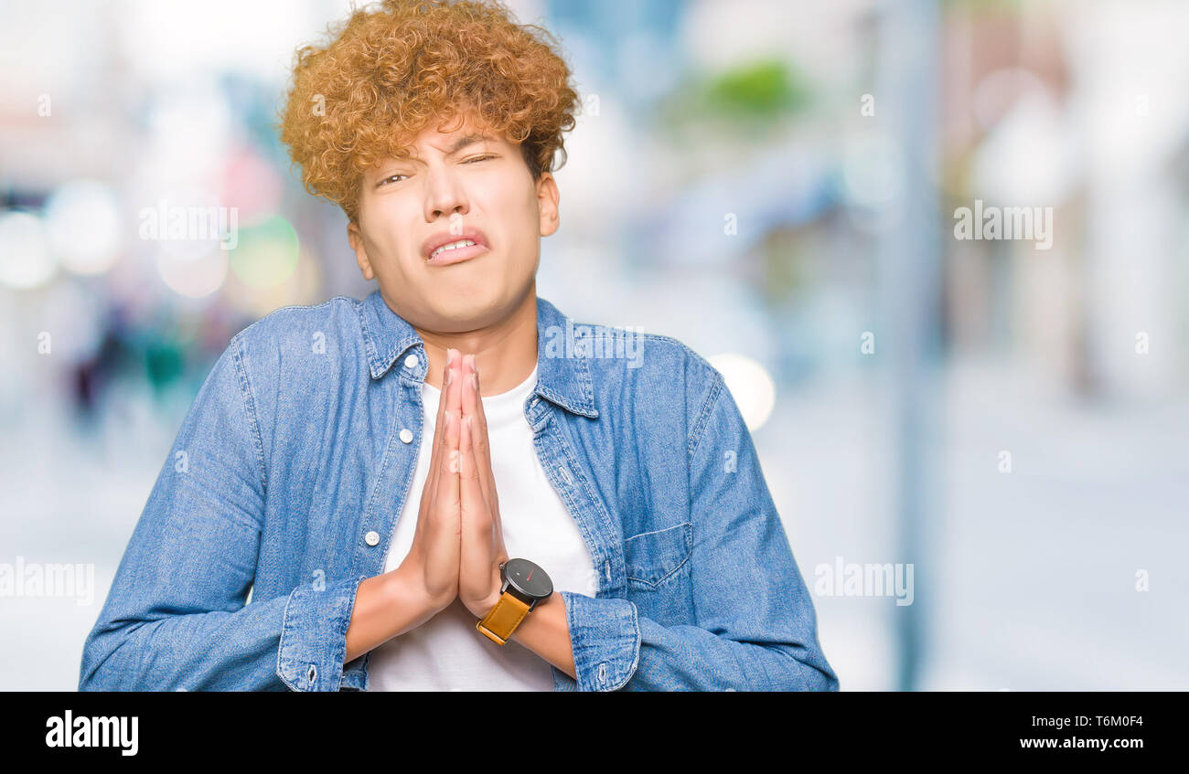 Young handsome man with afro hair wearing denim jacket begging and ...