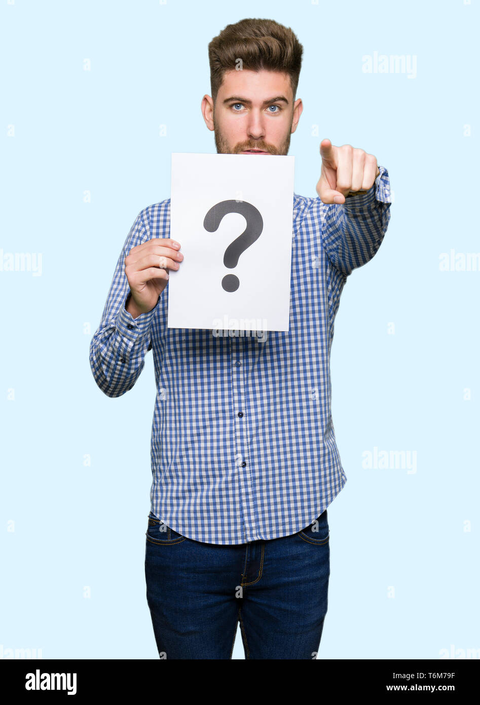 Young handsome man holding paper with question mark pointing with ...