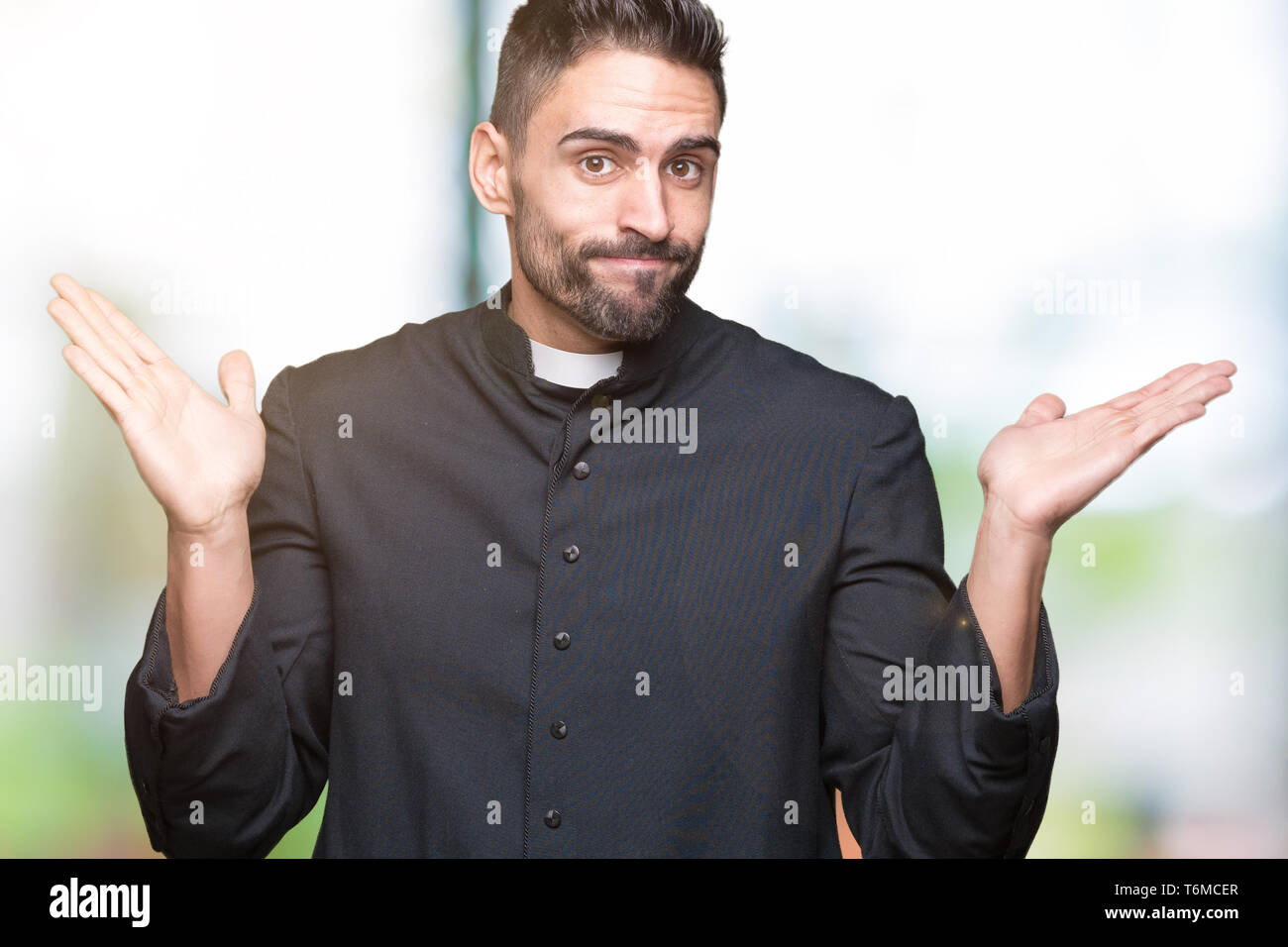 Young Christian priest over isolated background clueless and confused ...