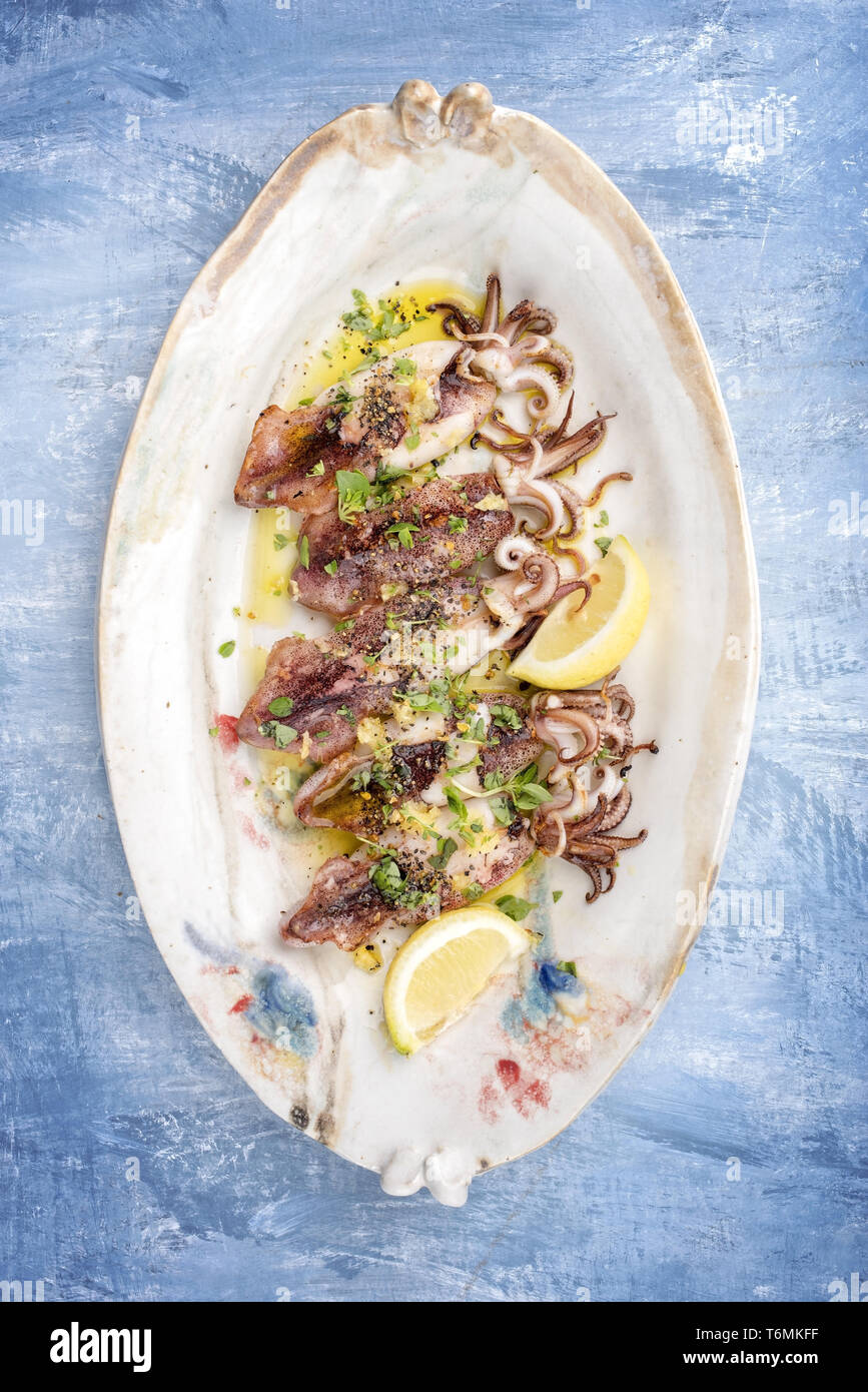 Traditional barbecue Greek calamari with herb and lemon as top view on ...