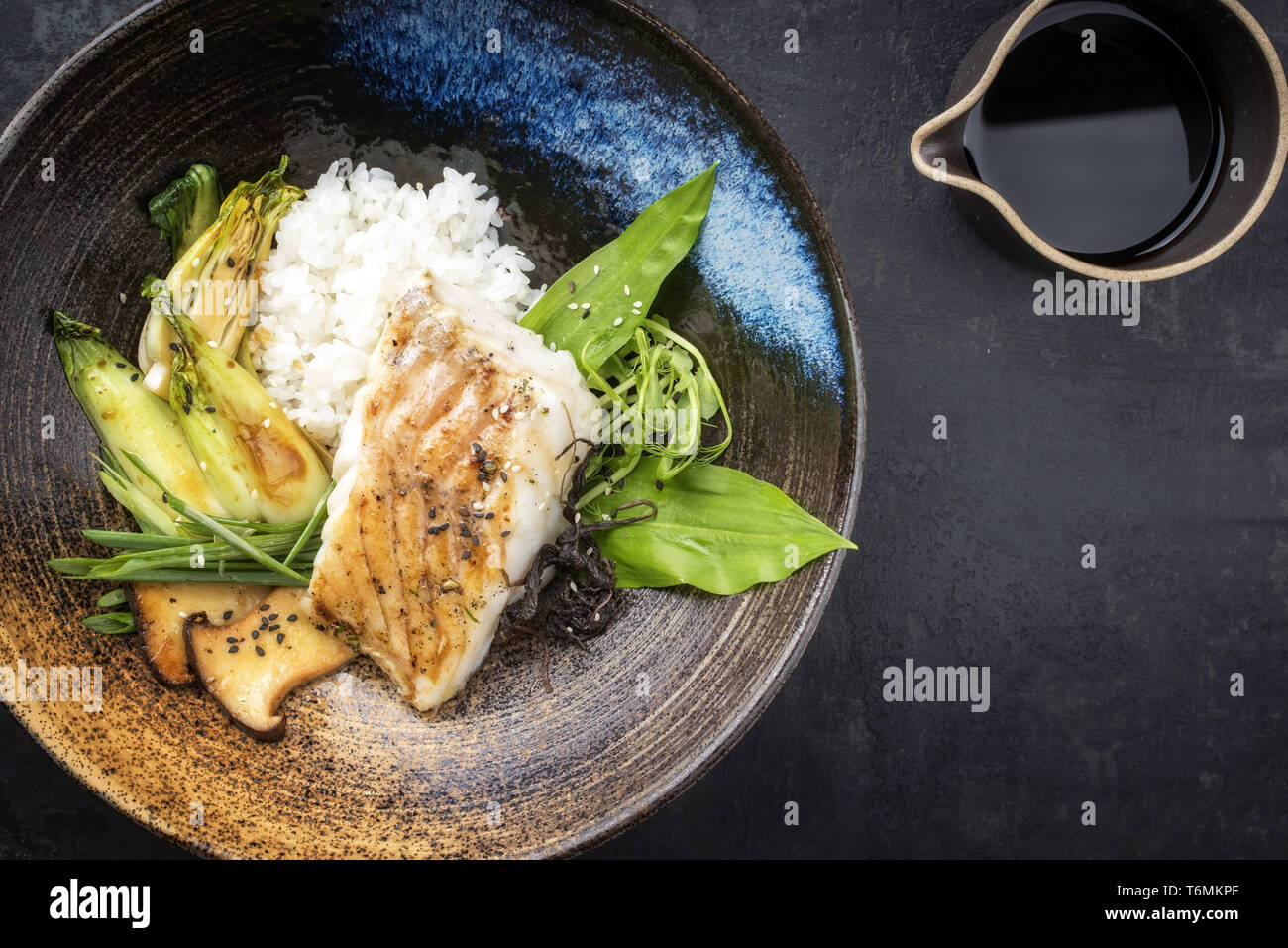 Modern Japanese fried cod fish filet with bok choi and rice as top view ...