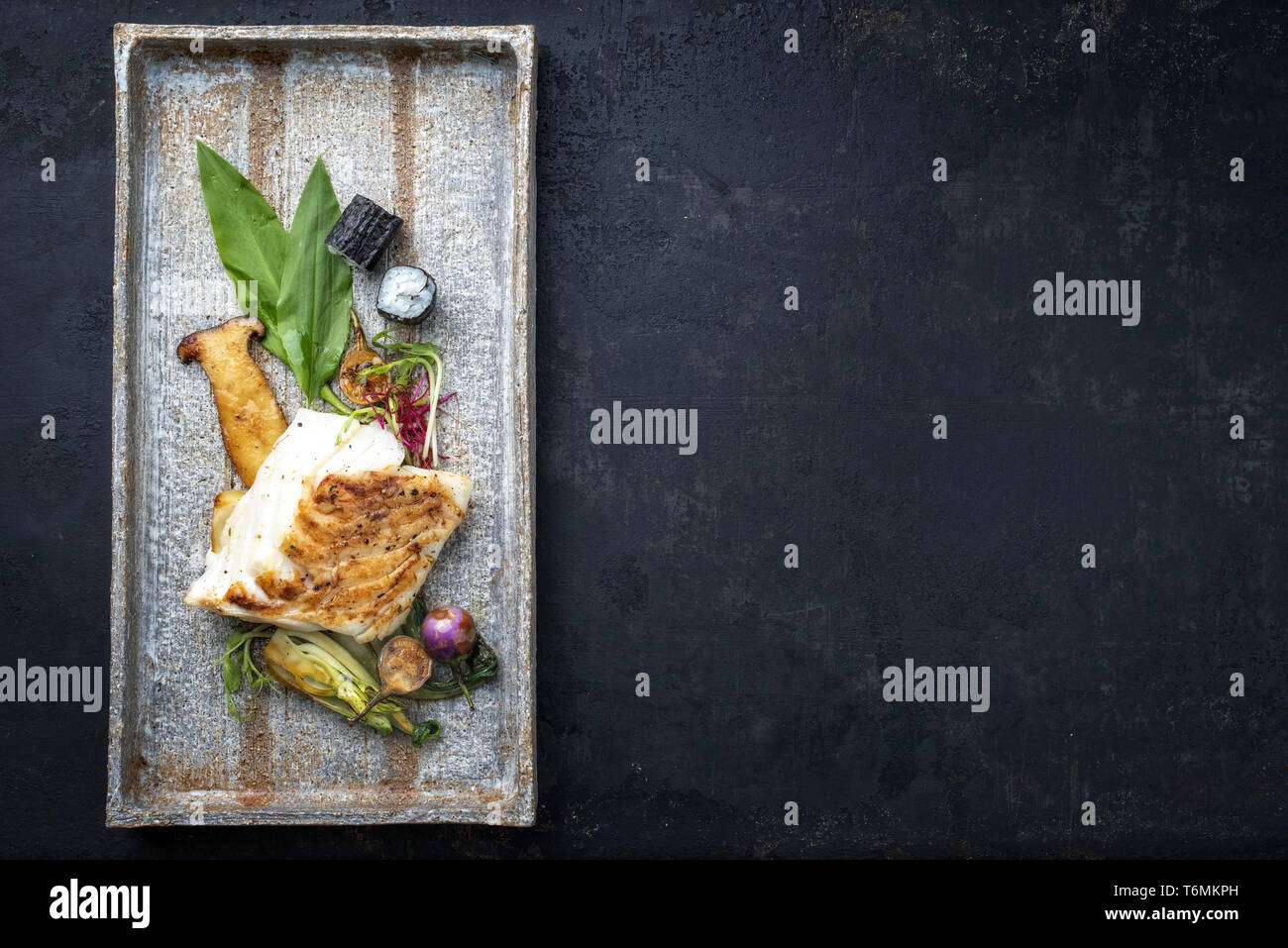 Modern Japanese fried cod fish filet with bok choi and sushi rolls as ...