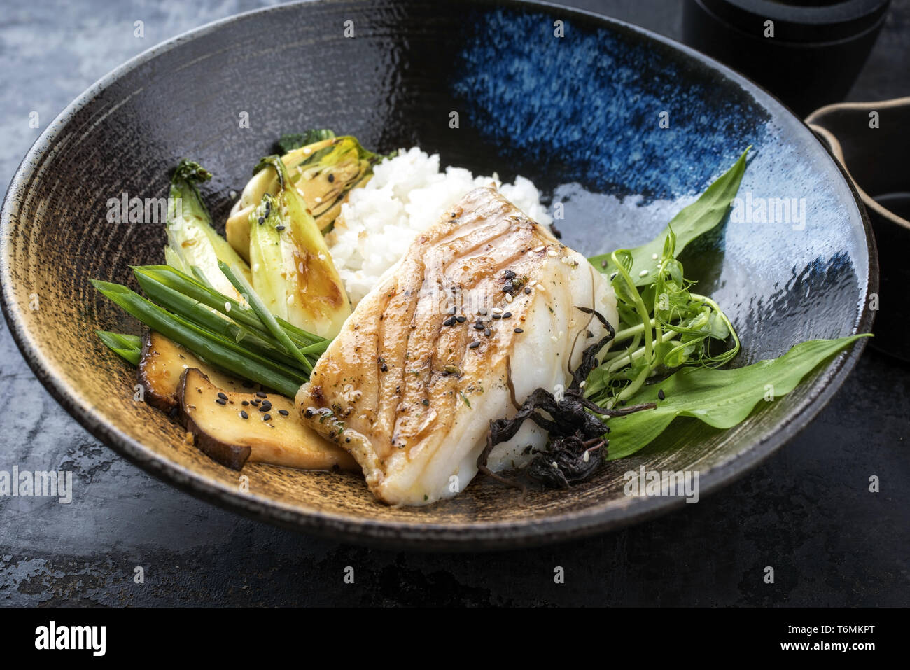 Modern Japanese fried cod fish filet with bok choi and rice as top view ...