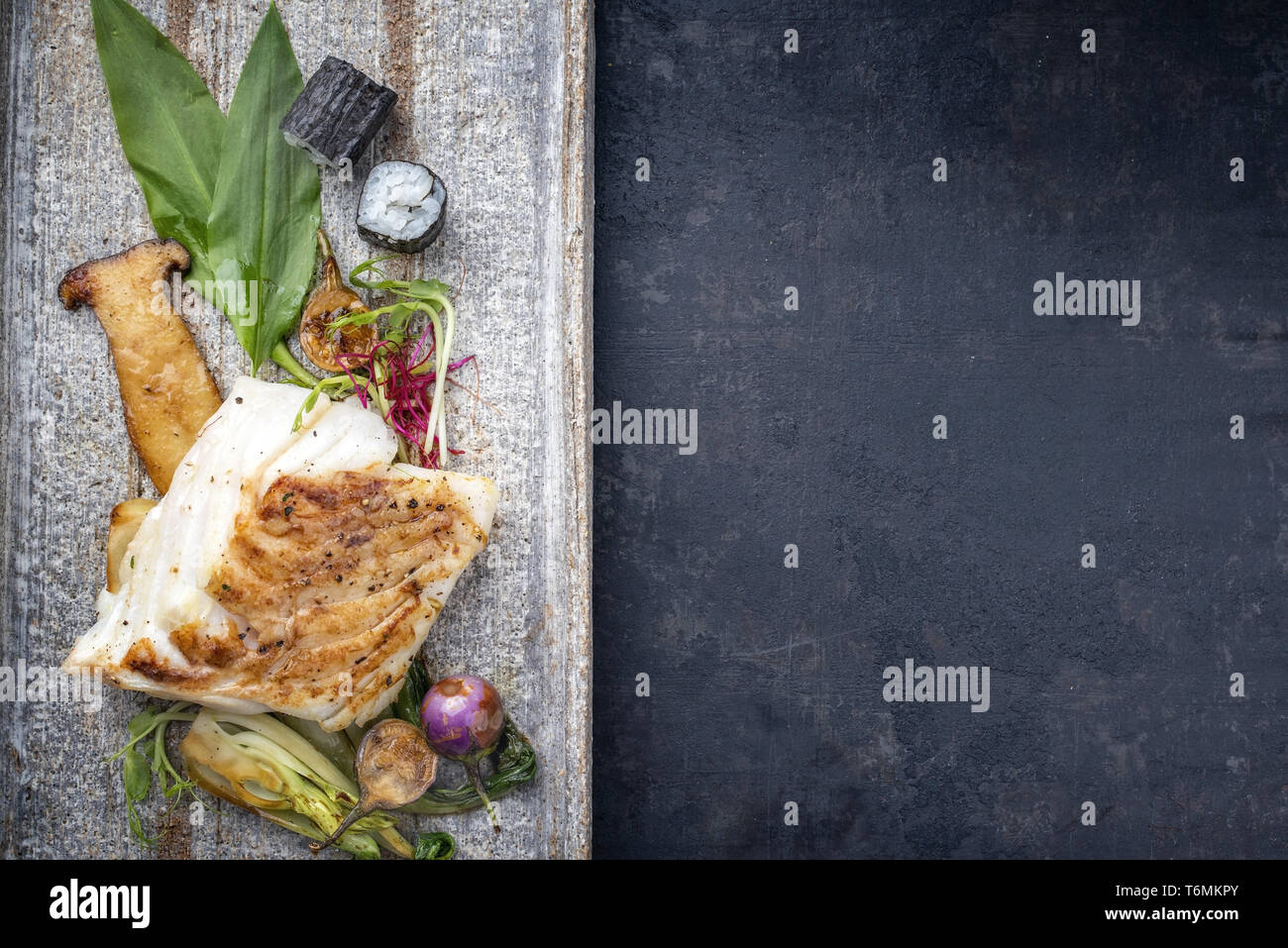 Modern Japanese fried cod fish filet with bok choi and sushi rolls as ...