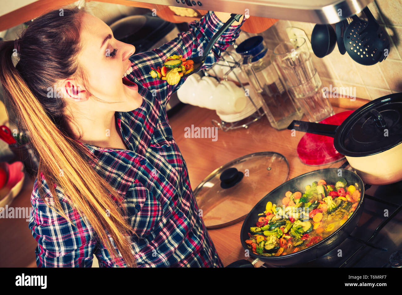Woman in kitchen cooking stir fry frozen vegetables and tasting. Girl ...