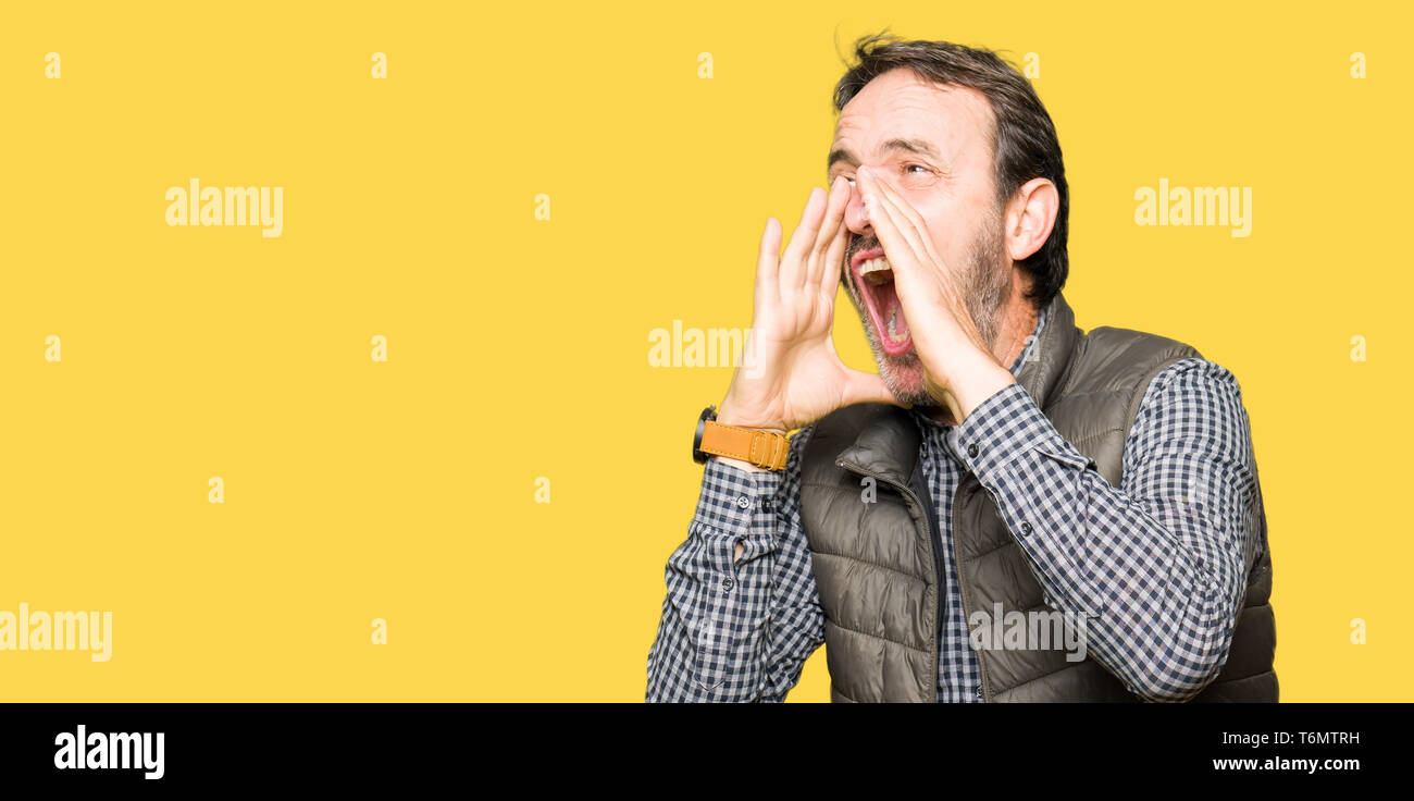 Middle age handsome man wearing winter vest Shouting angry out loud ...