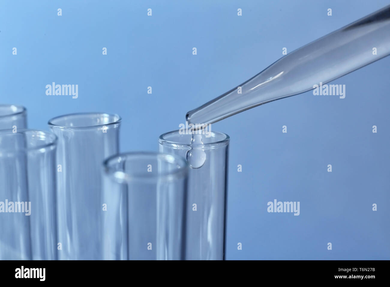 Pipette dripping sample into test tube on color background, closeup ...